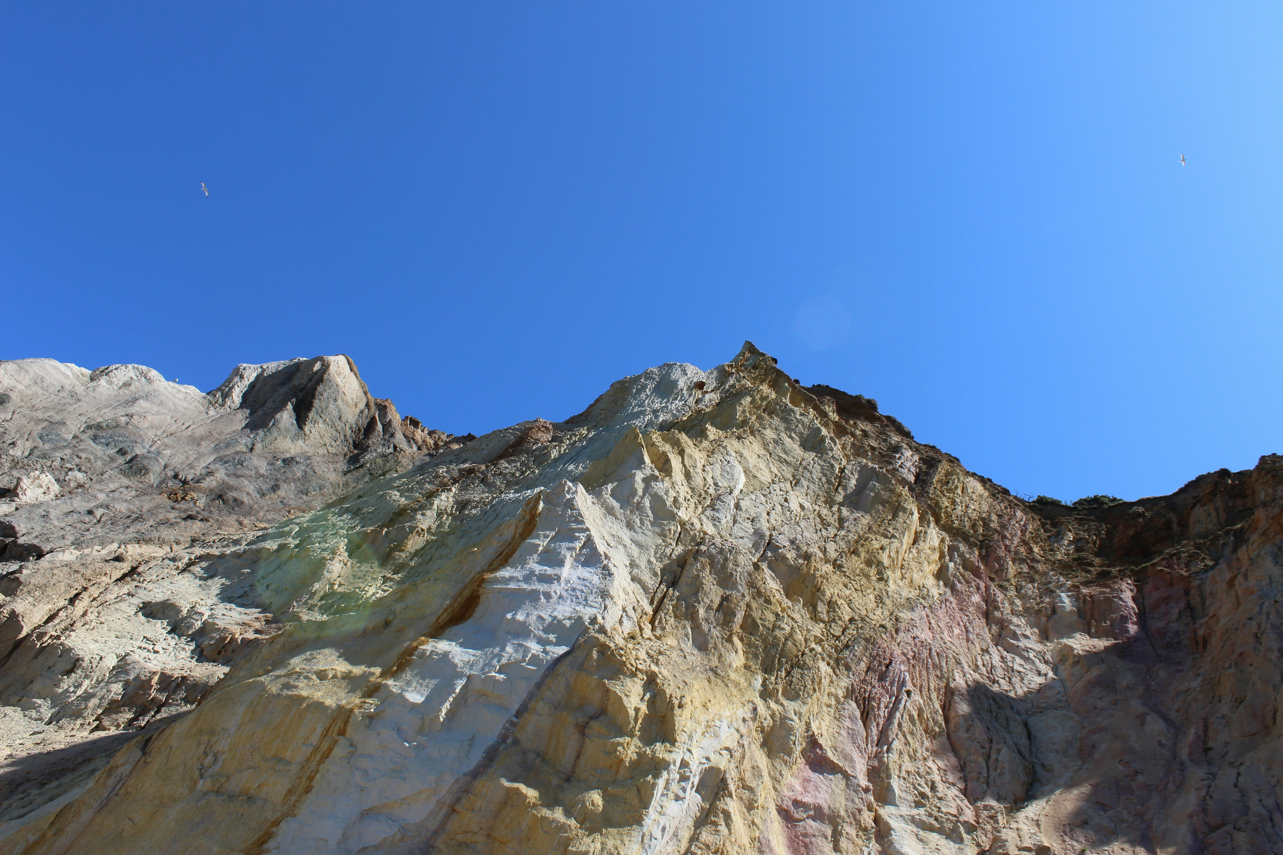 Vibrant layers of mineral-rich rock formations rise against a clear blue sky, showcasing the Earth's geological artistry.