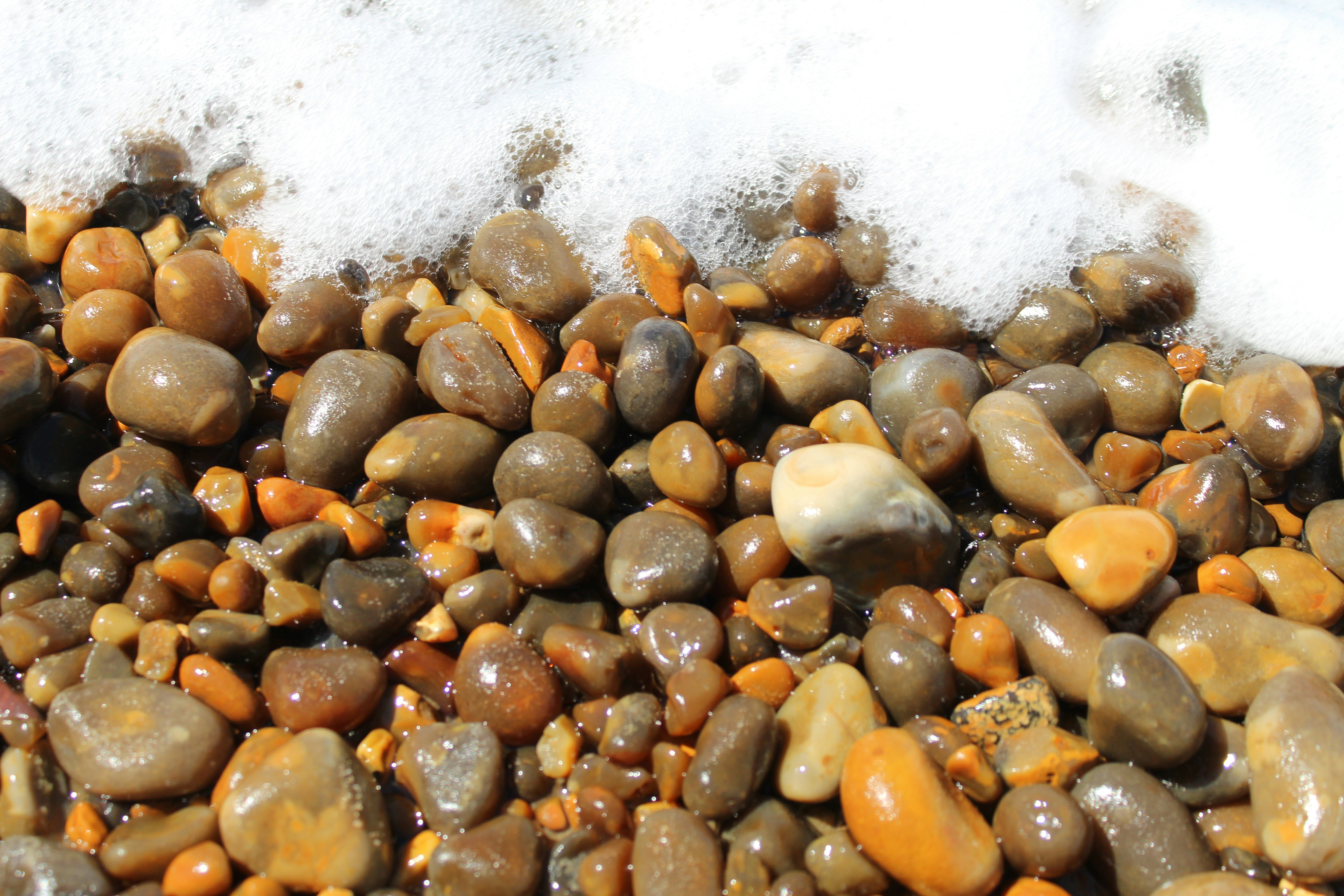 Pebbles are on the beach with the foamy ocean.
