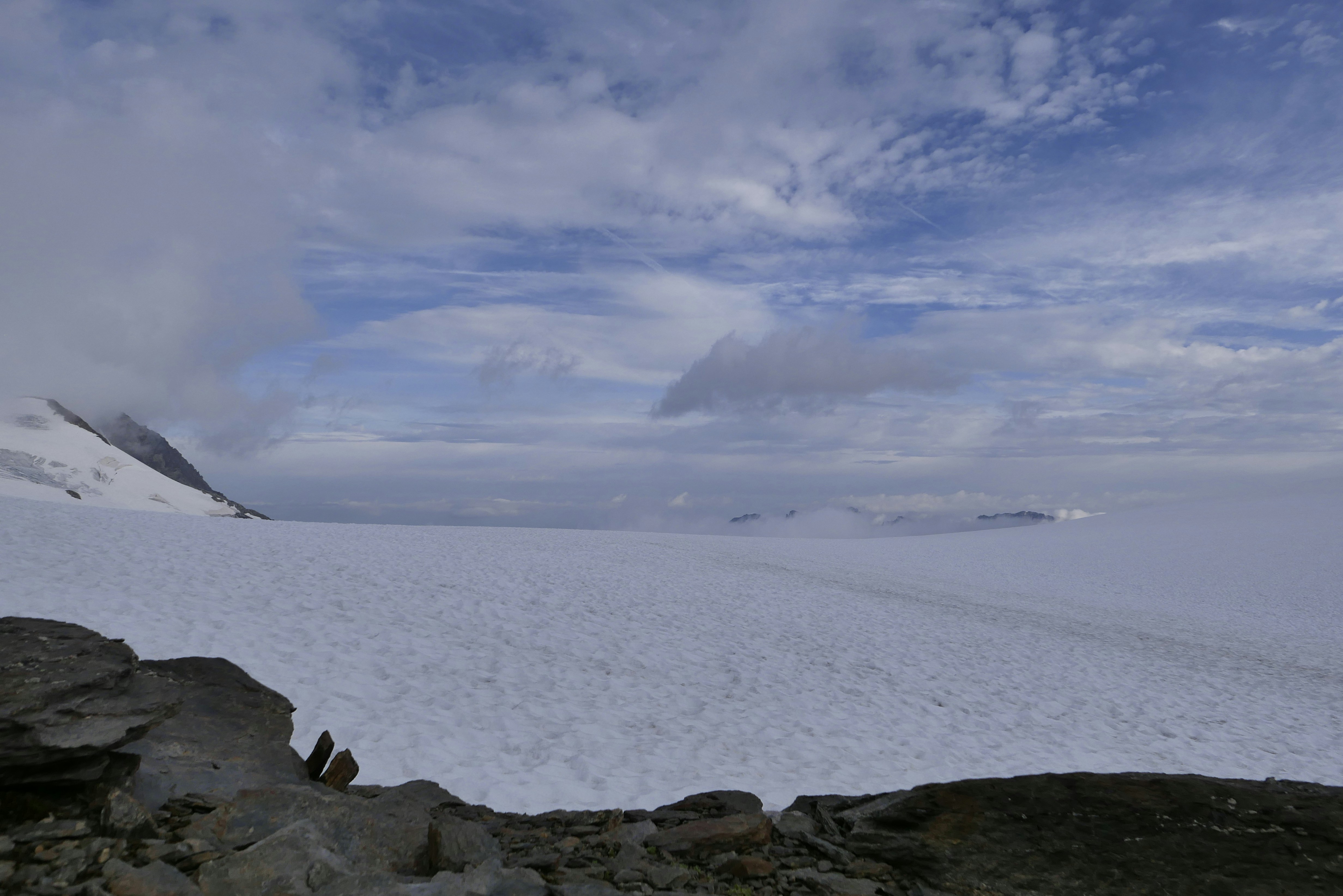 Vast expanse of snow-covered glacier under a cloudy sky, with rocky foreground leading into the horizon. 