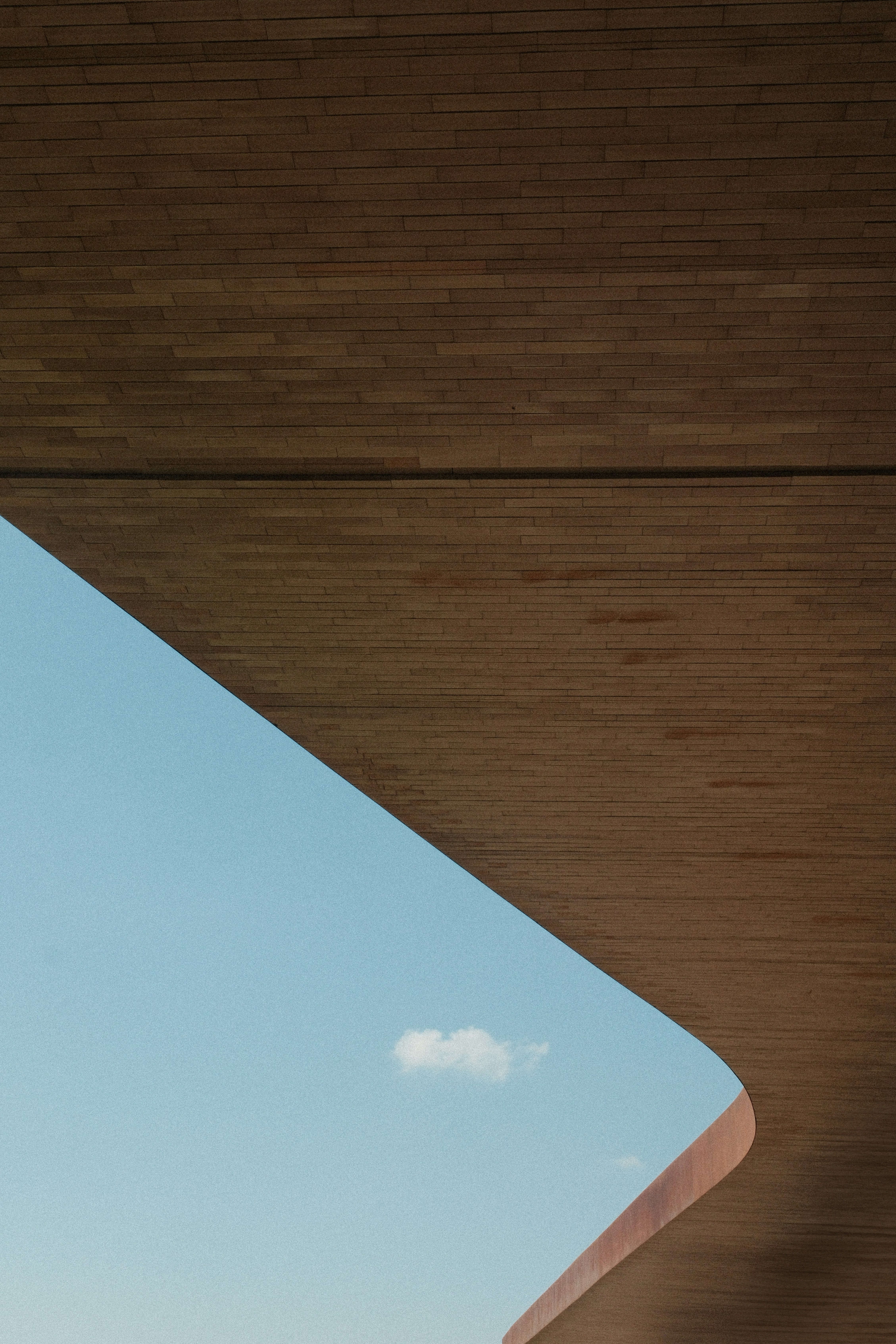 Abstract architectural detail showcasing a curved overhang against a blue sky with scattered clouds.