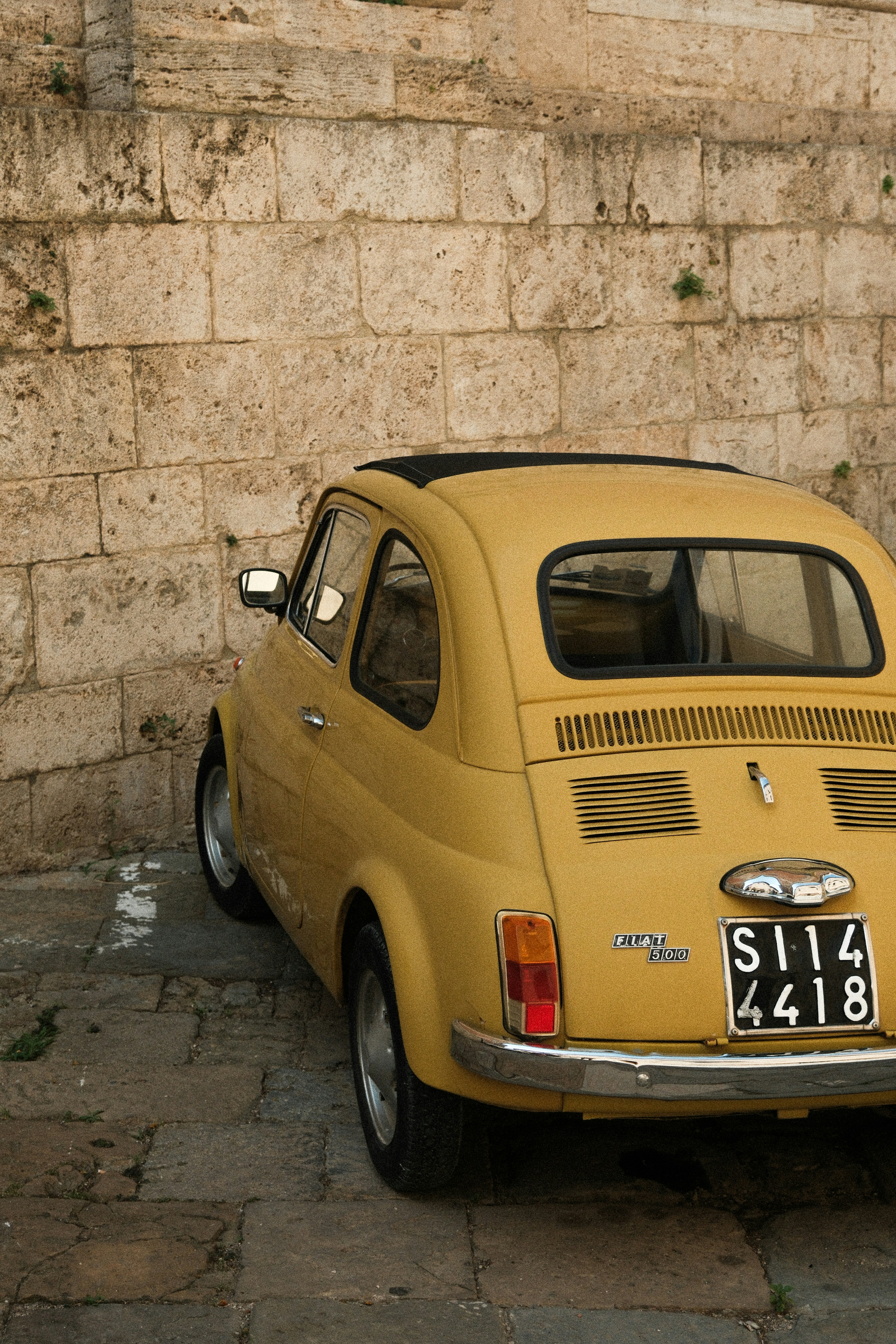 A yellow vintage fiat parked near a stone wall.