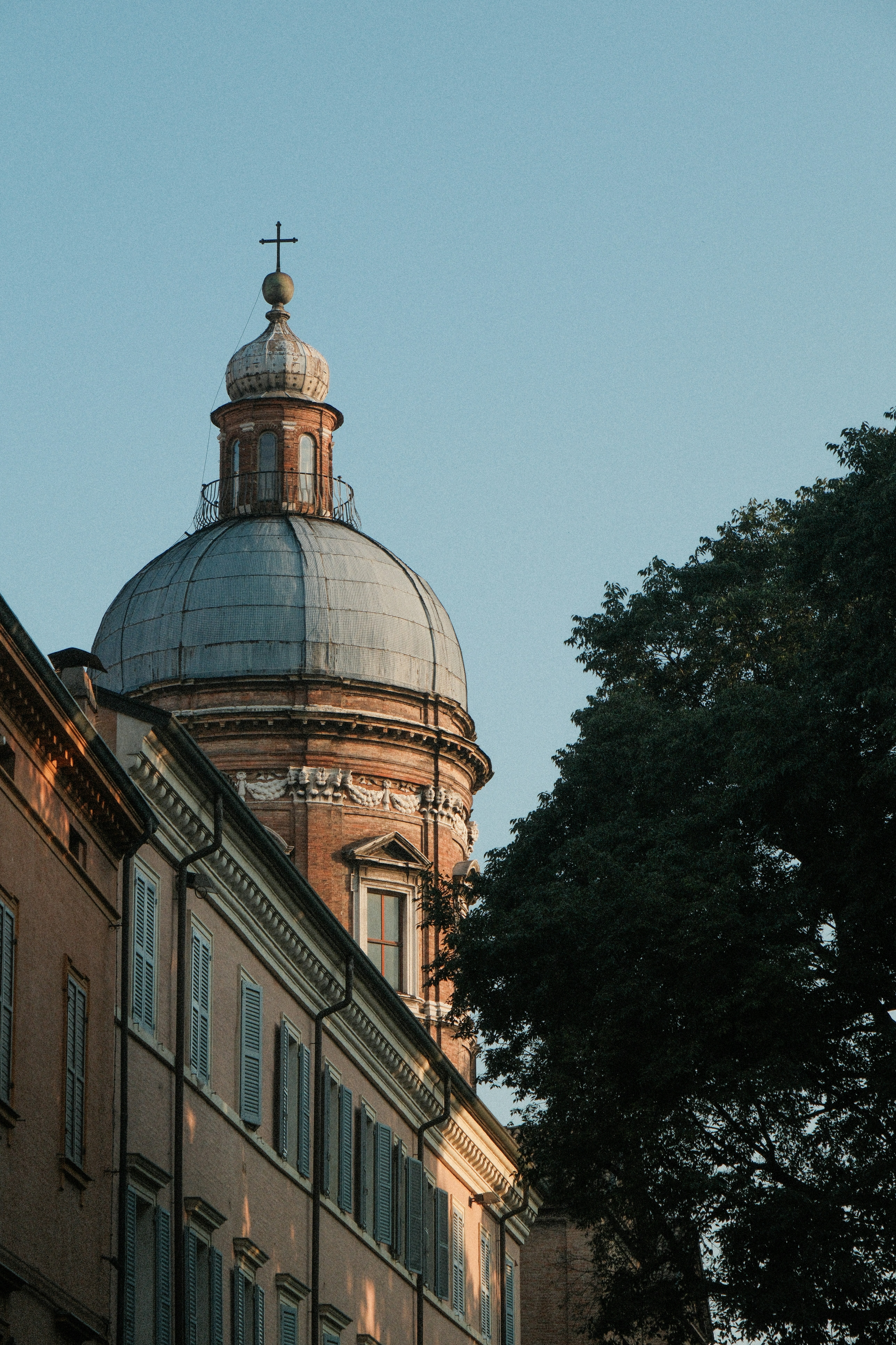 Historic dome of a church peeks above a tree, bathed in warm evening light. The architectural details showcase classic design elements.