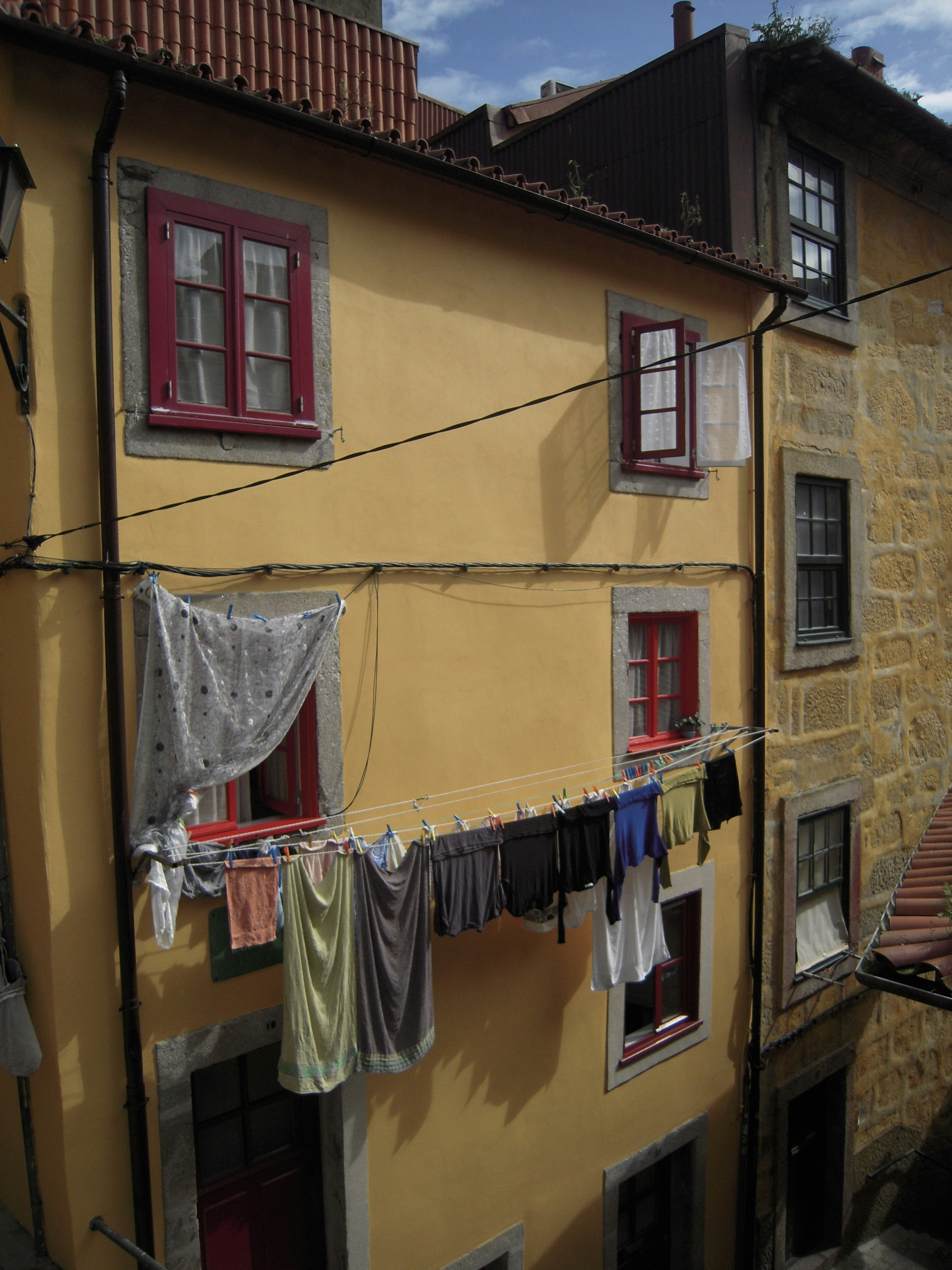 Colorful laundry hanging between buildings in a narrow alley, showcasing the charm of urban life. The vibrant yellow walls contrast with the hues of the clothes.