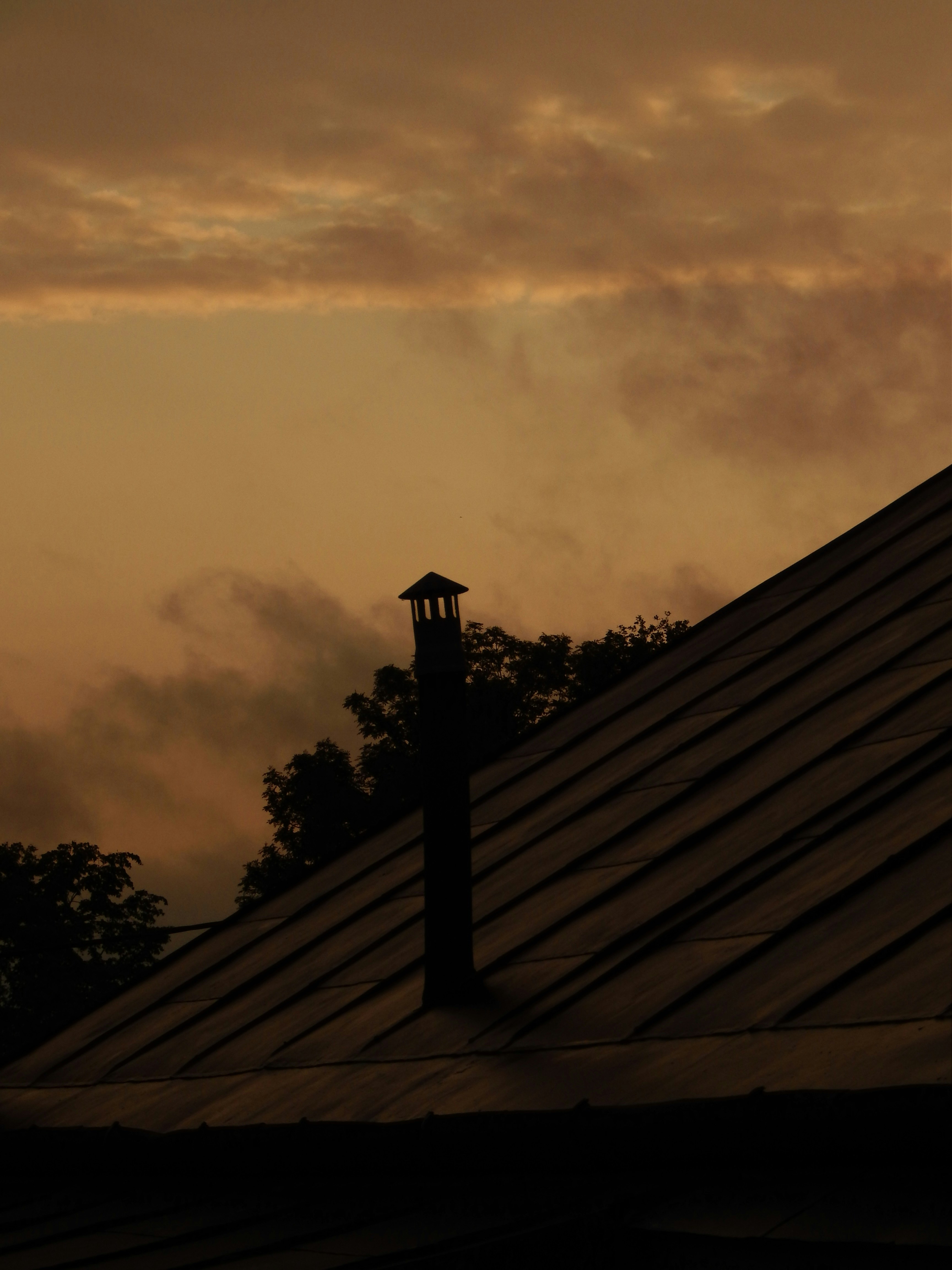 Silhouette of a roof and chimney at dusk.