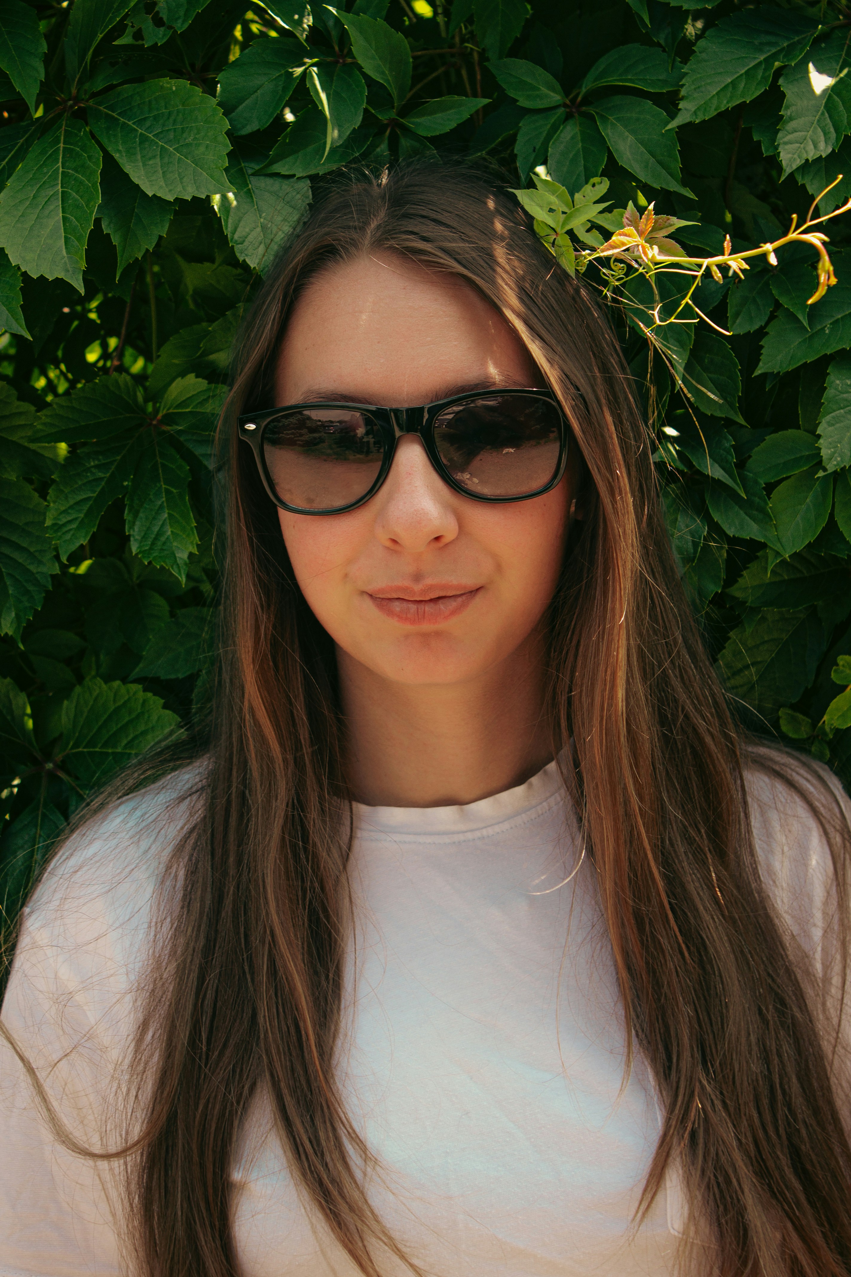 Young woman in sunglasses poses in front of leaves.