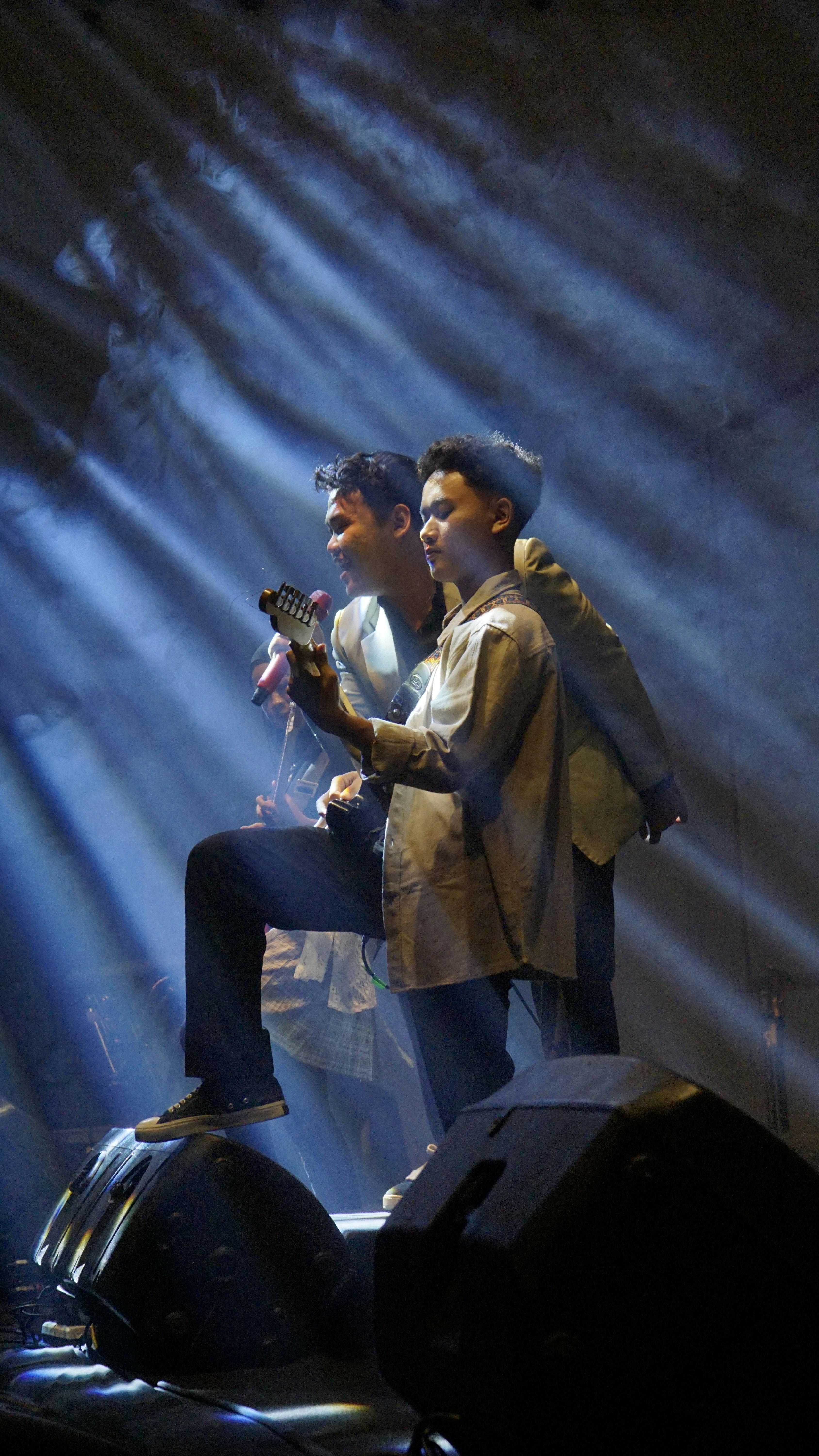 Two men sing on stage under stage lights.