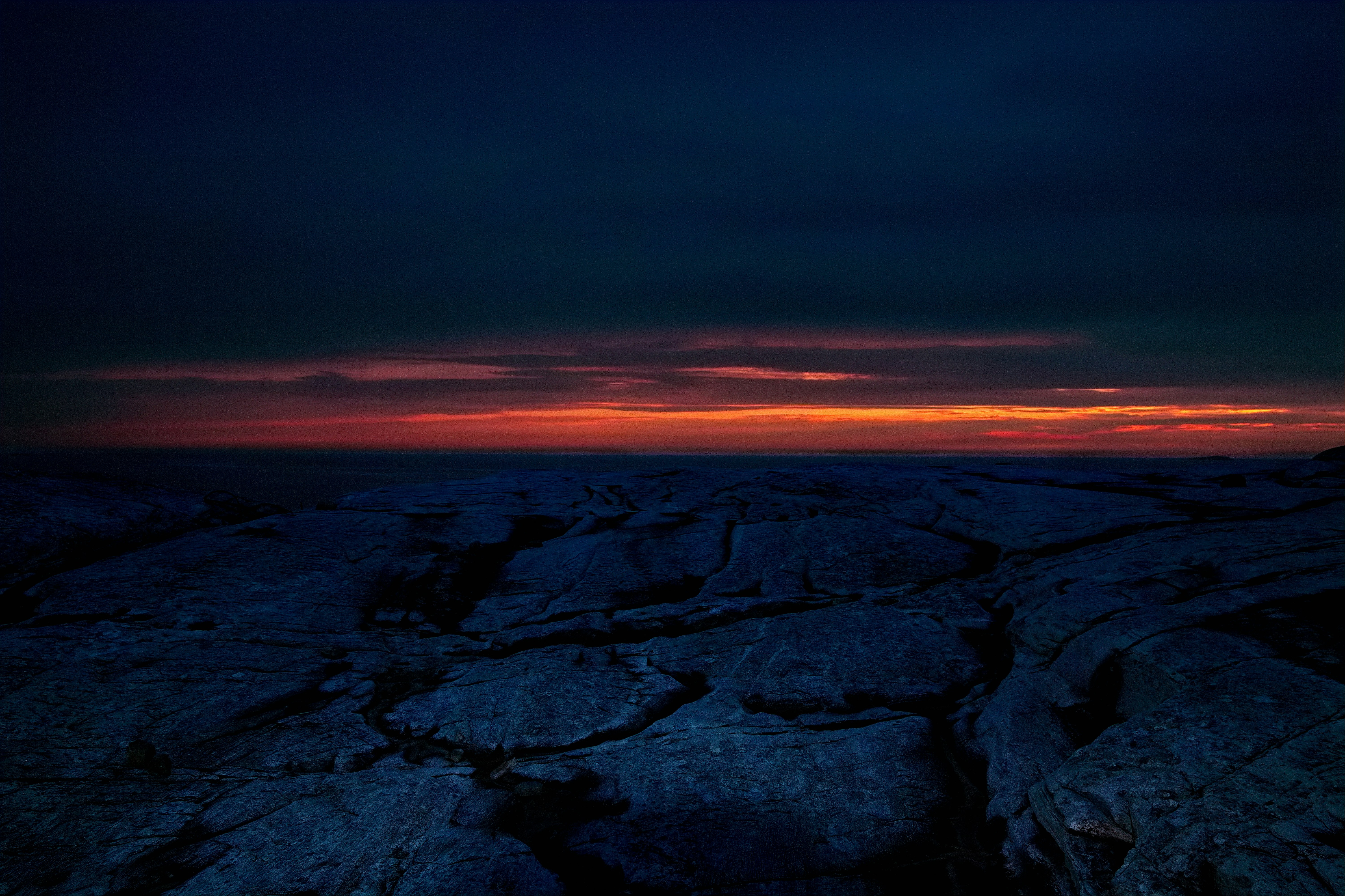Vast rocky landscape illuminated by a vibrant twilight sky, showcasing a gradient of deep blues and warm oranges. The scene captures the serene transition from day to night.