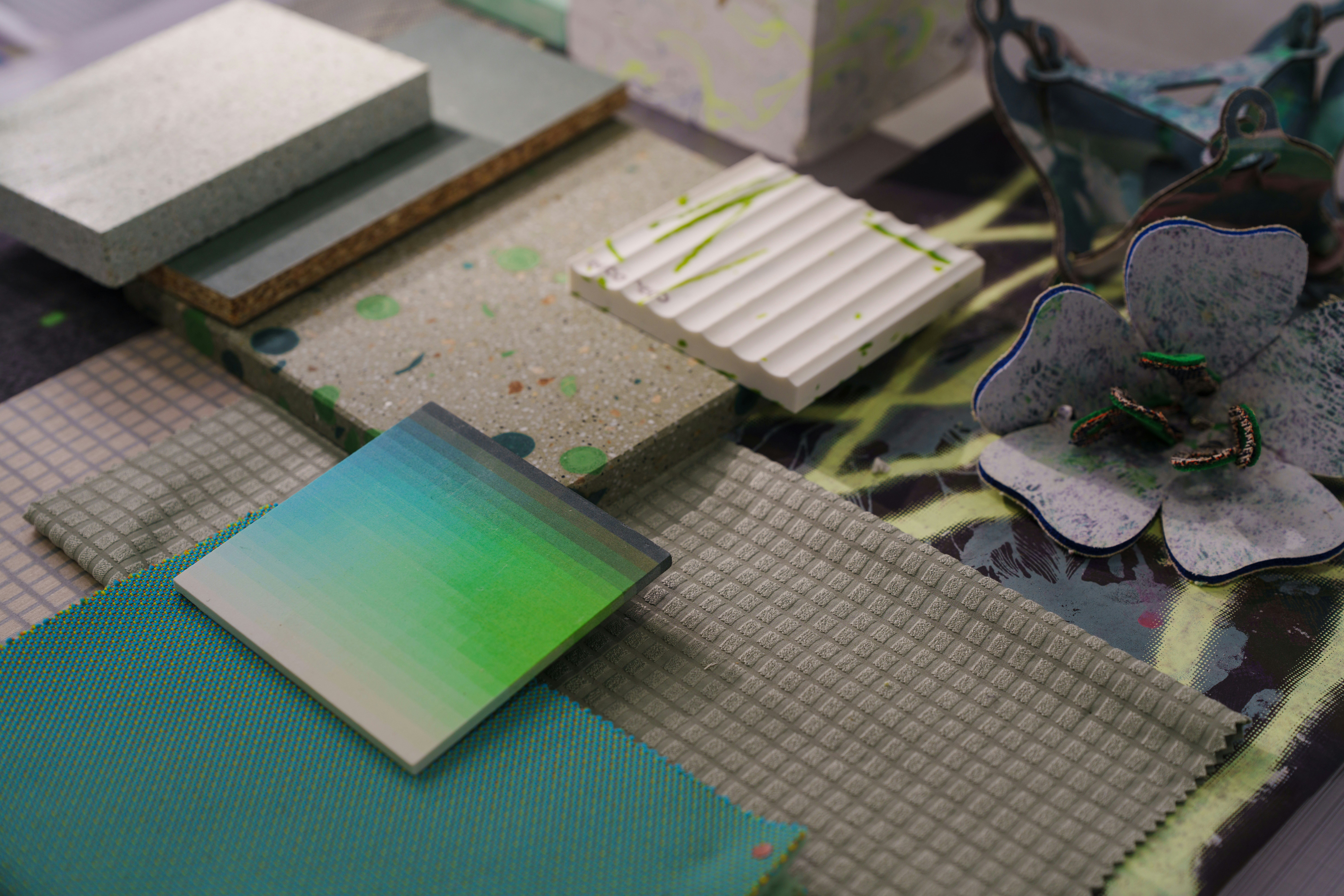 Small tile swatches and craft materials arranged on a textured work surface, capturing color blocks and patterns in a close-up setup.