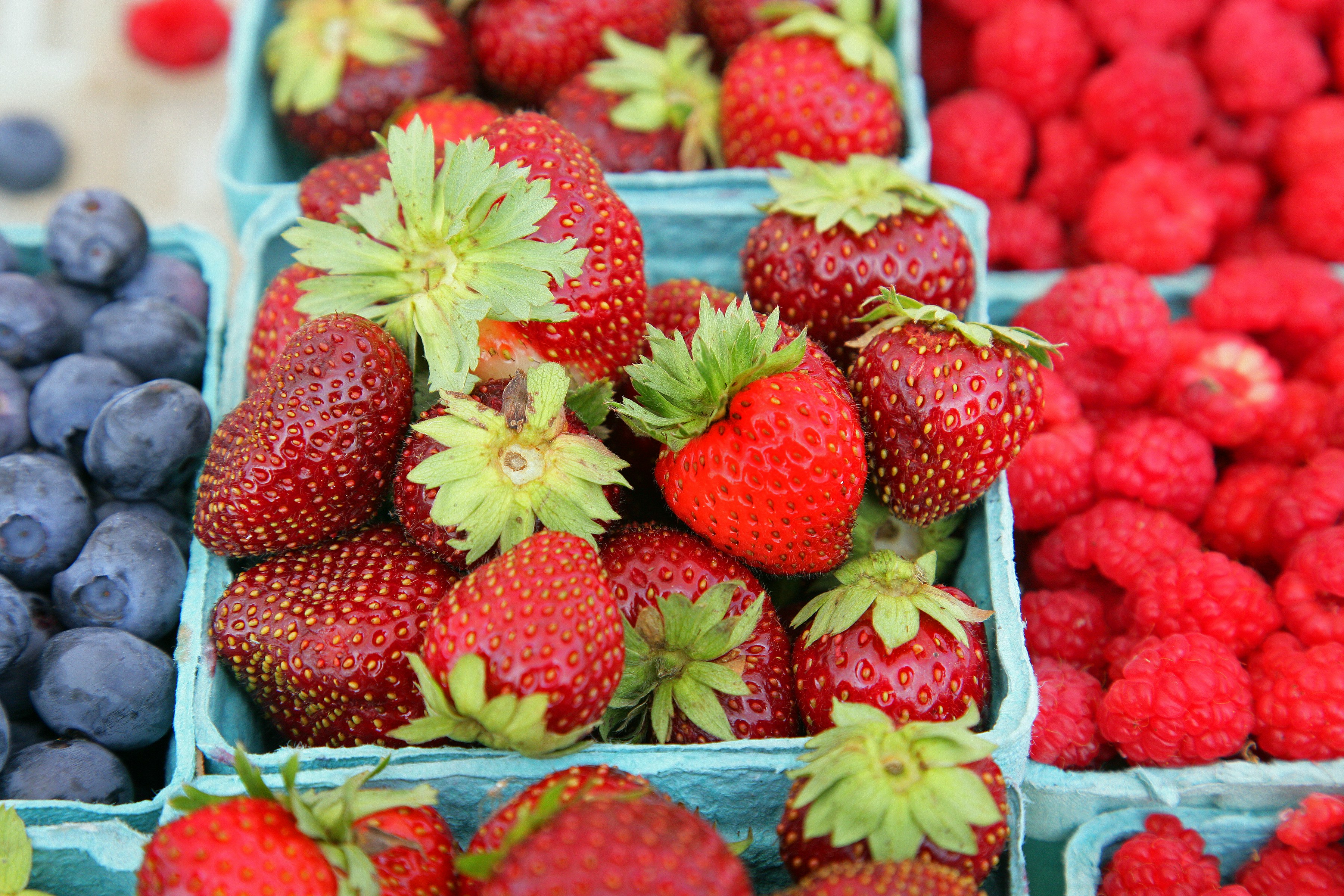 Vibrant strawberries nestled among blueberries and raspberries in a market display, showcasing the abundance of fresh fruit.