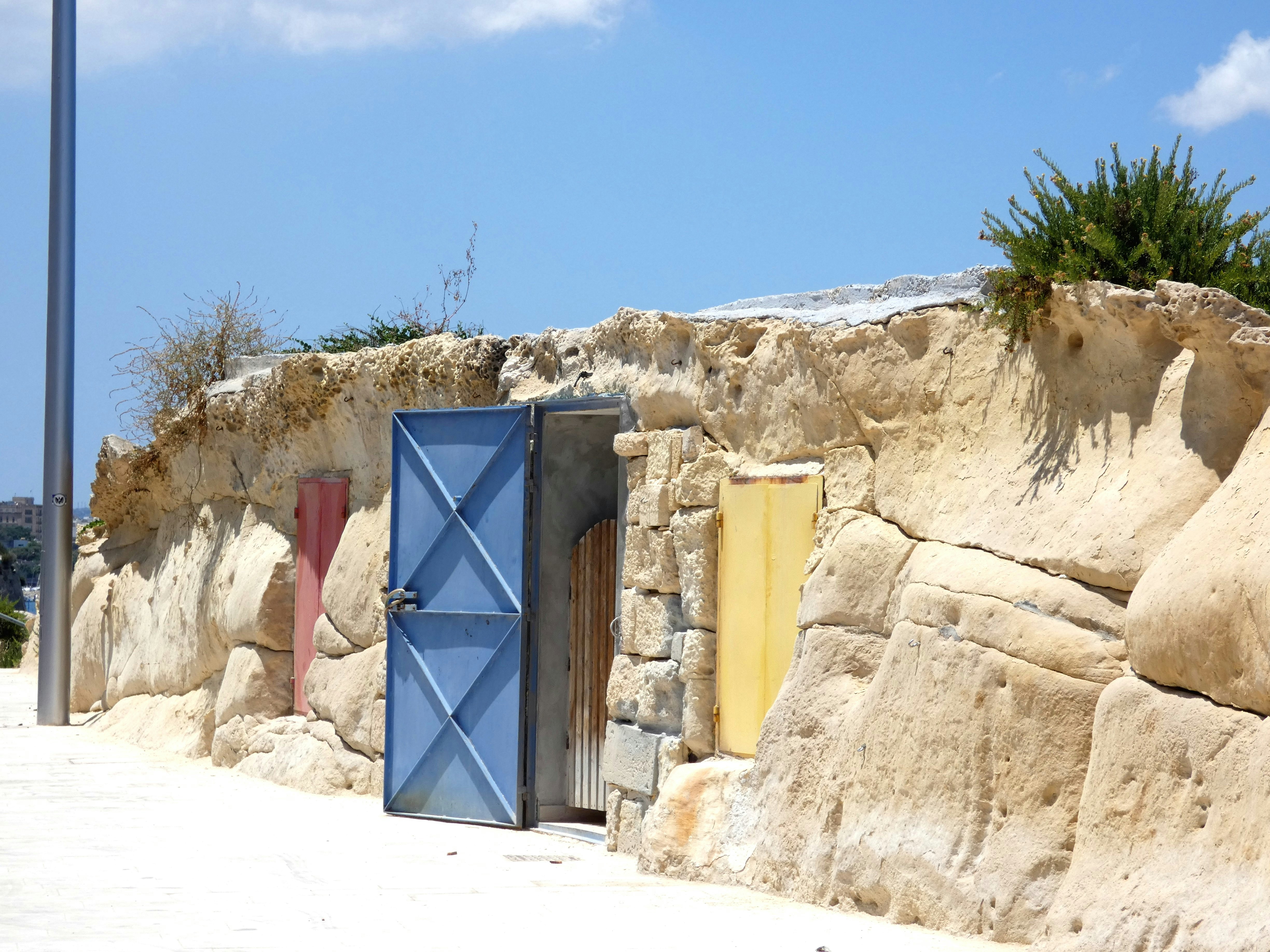 Sunny day, Valletta, Light | Colorful doors are nestled into a rocky cliffside.