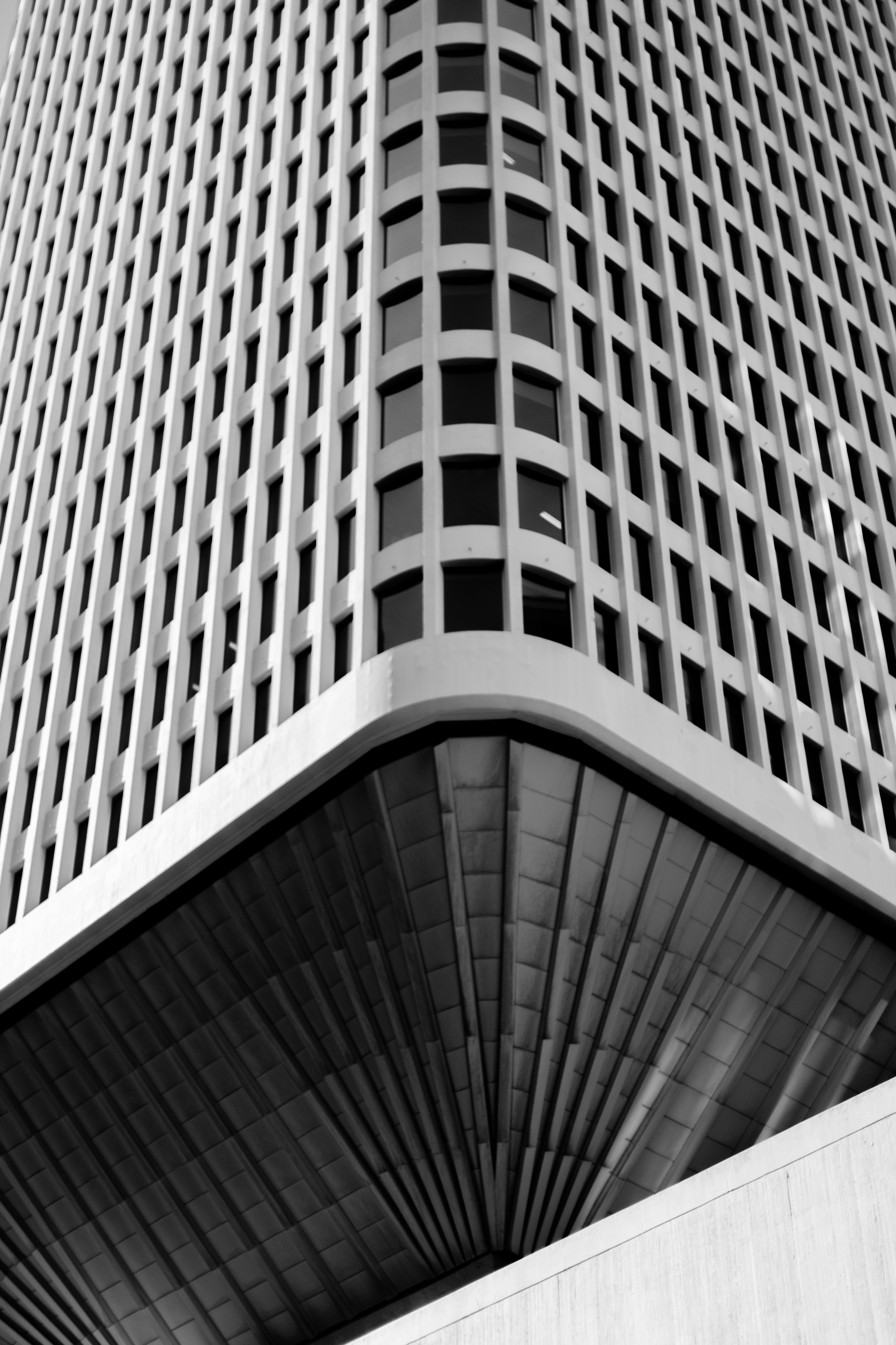 Abstract view of a modern building's underside, showcasing geometric patterns and contrasting textures in monochrome.