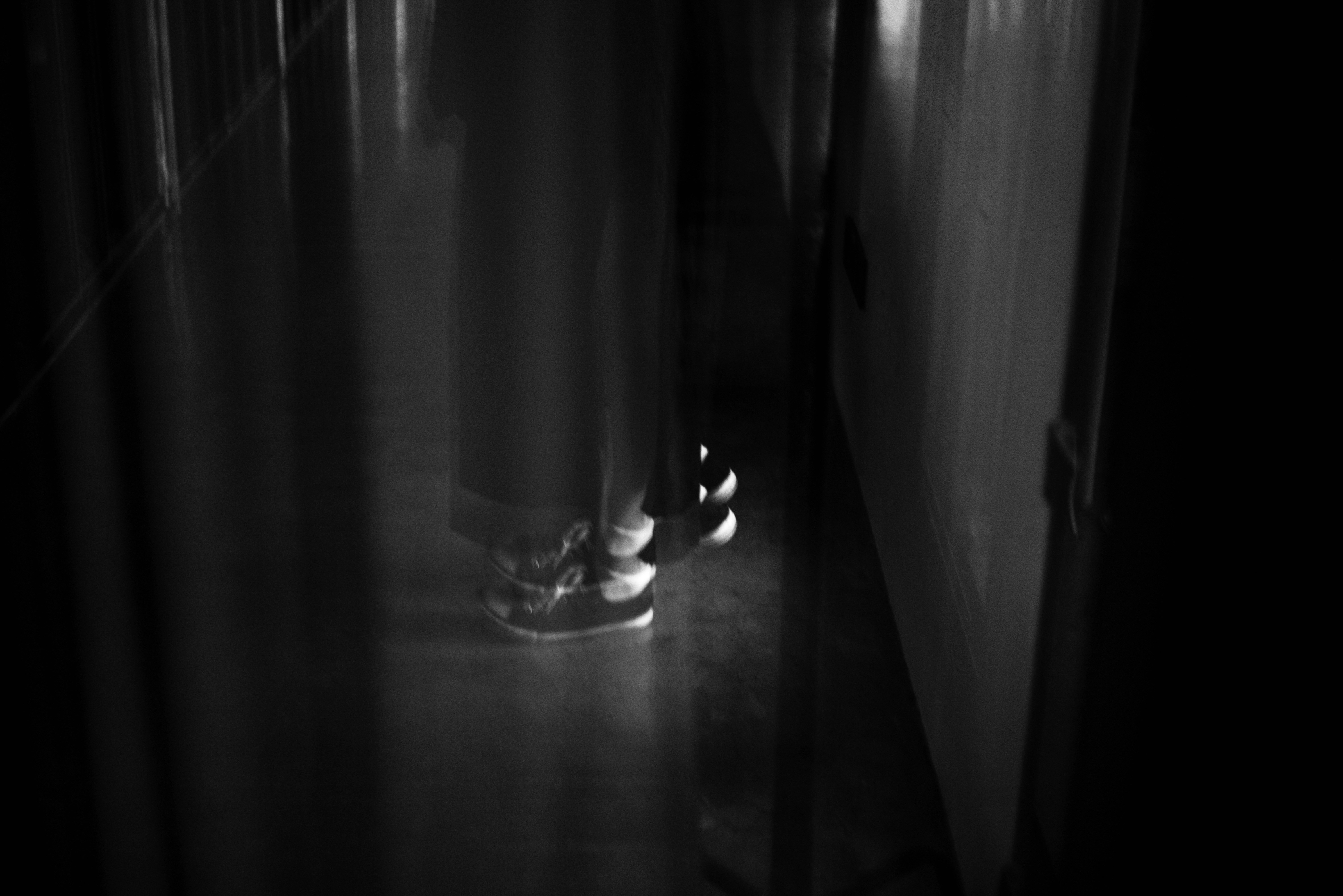 Shadowy figures partially obscured by a curtain in a dimly lit corridor.