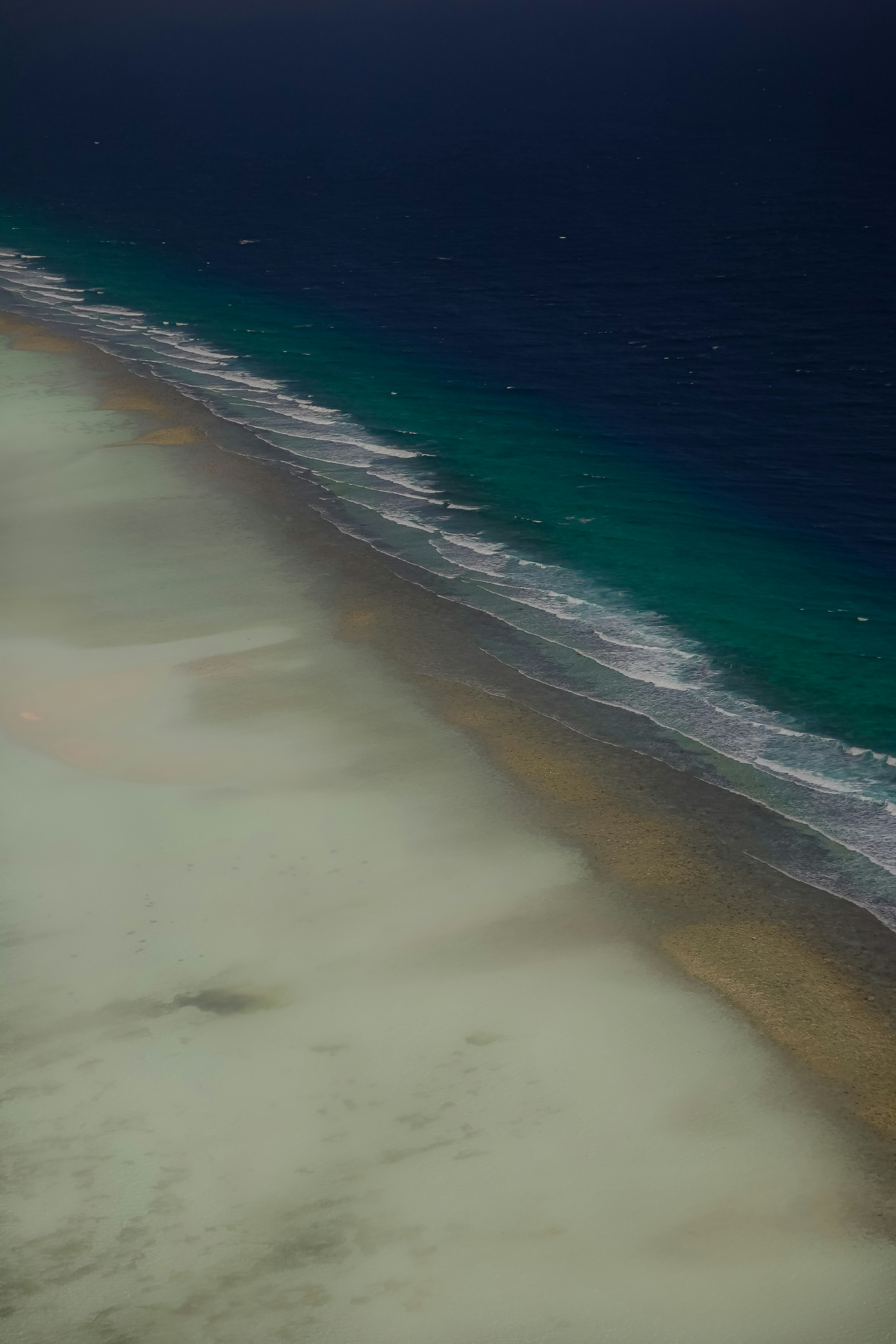 Aerial view of a tranquil shoreline where turquoise waves meet sandy shallows, creating a mesmerizing gradient of colors.