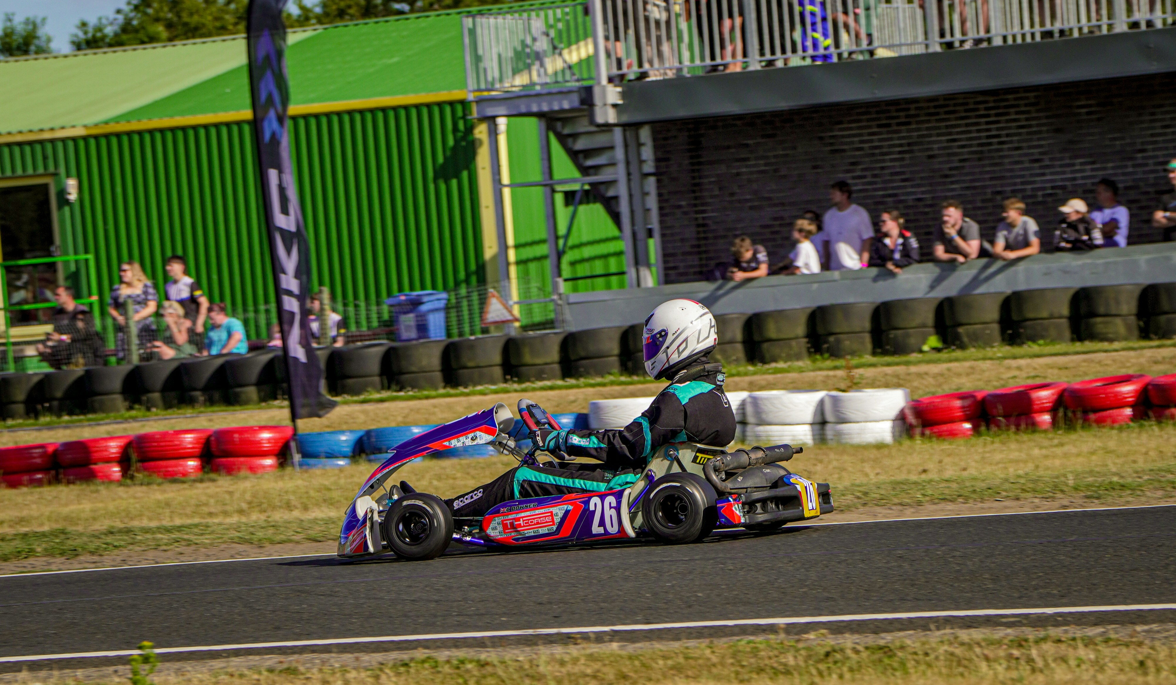 Apex Rush: Kart 26 Slices the Track Past Tire Barriers as Spectators Look On