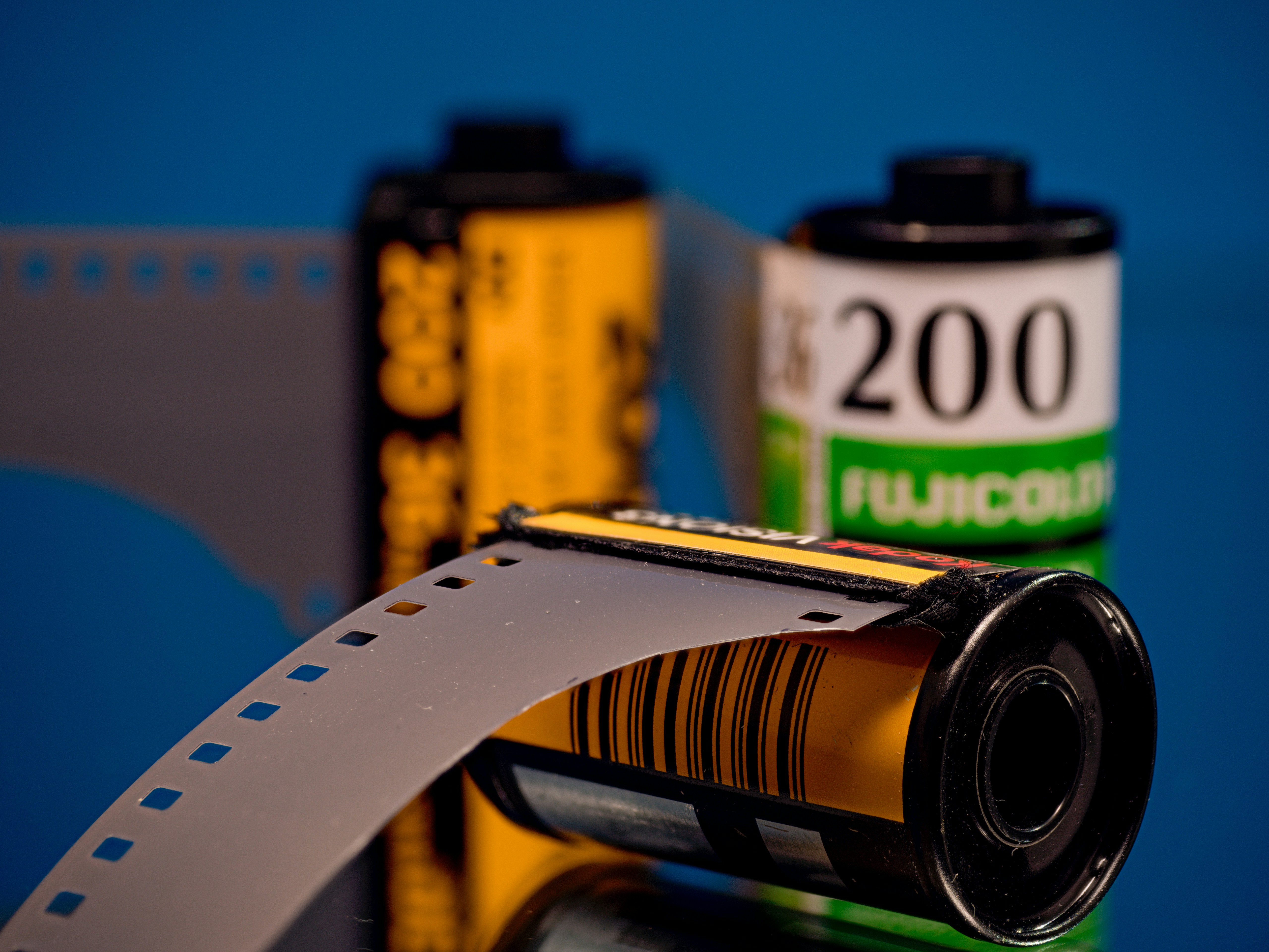 Three film canisters, including Fujicolor 200, with a strip of film elegantly unfurling in the foreground.