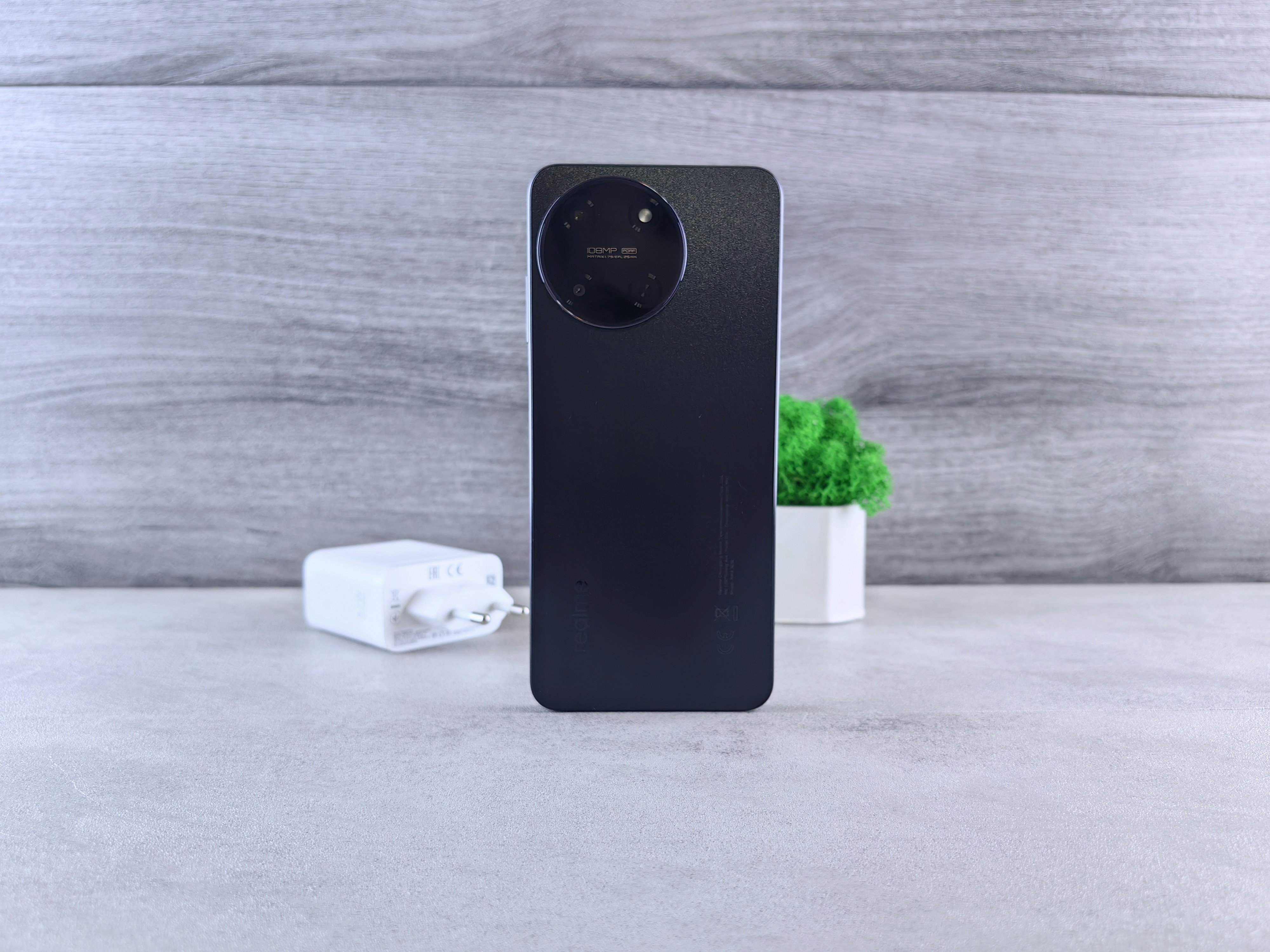 Huawei P60 Pro smartphone positioned upright against a textured backdrop, accompanied by a small plant and charger. The sleek design showcases its modern aesthetics.