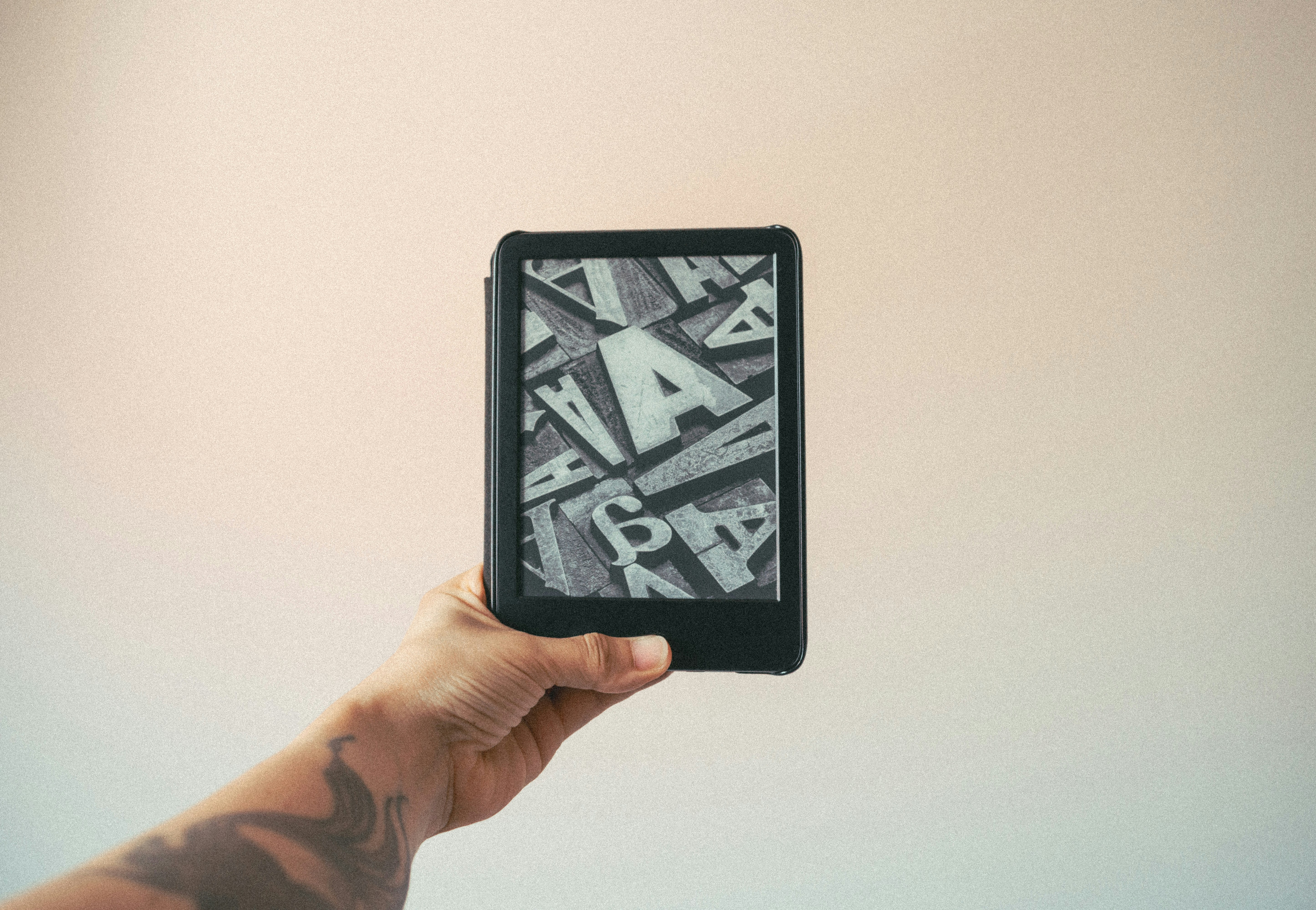 Hand holding an e-reader displaying letters.
