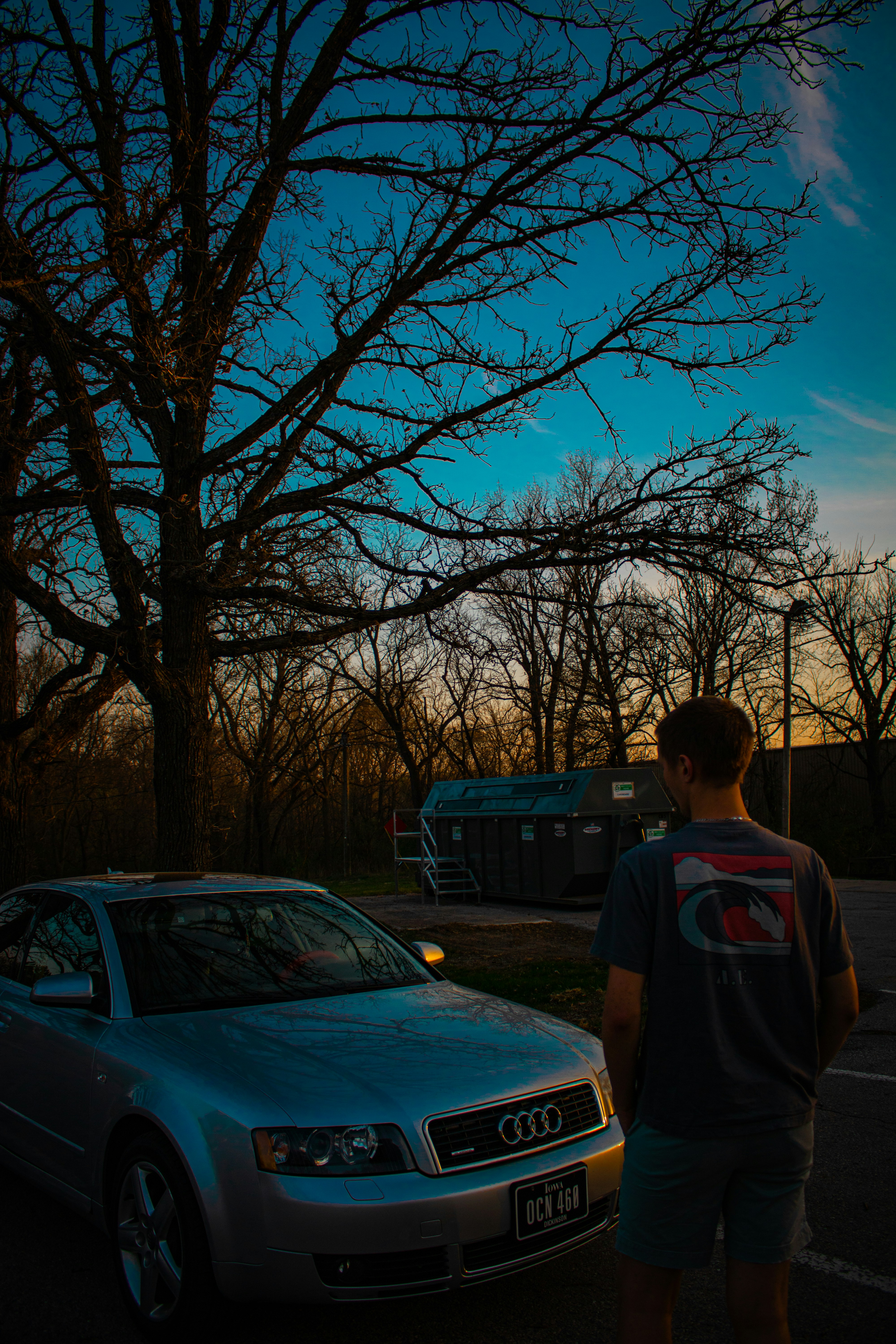 A man gazes at an audi under a blue sky.