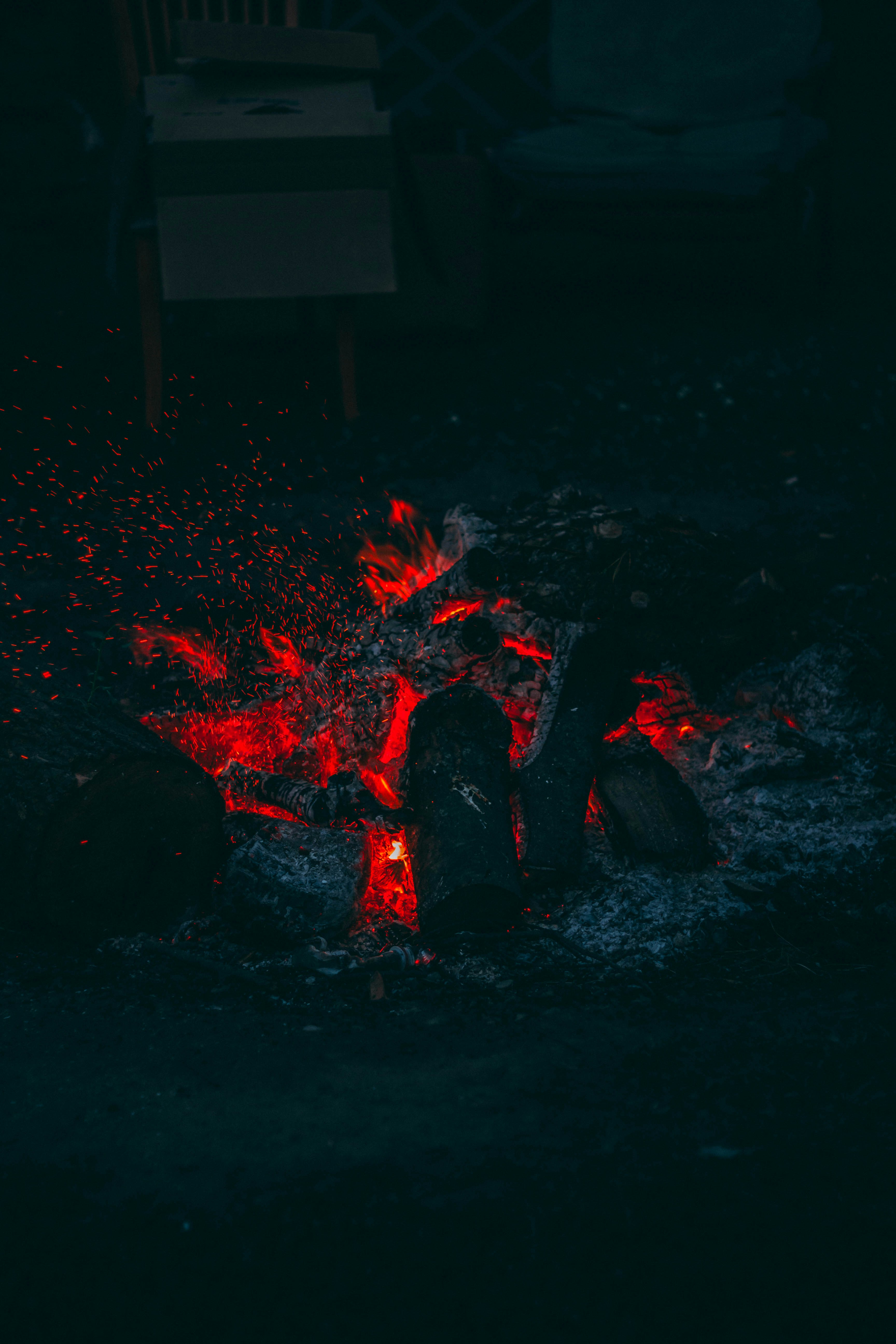 Glowing embers and scattered sparks from a campfire, creating a warm yet mysterious ambiance in the darkness.