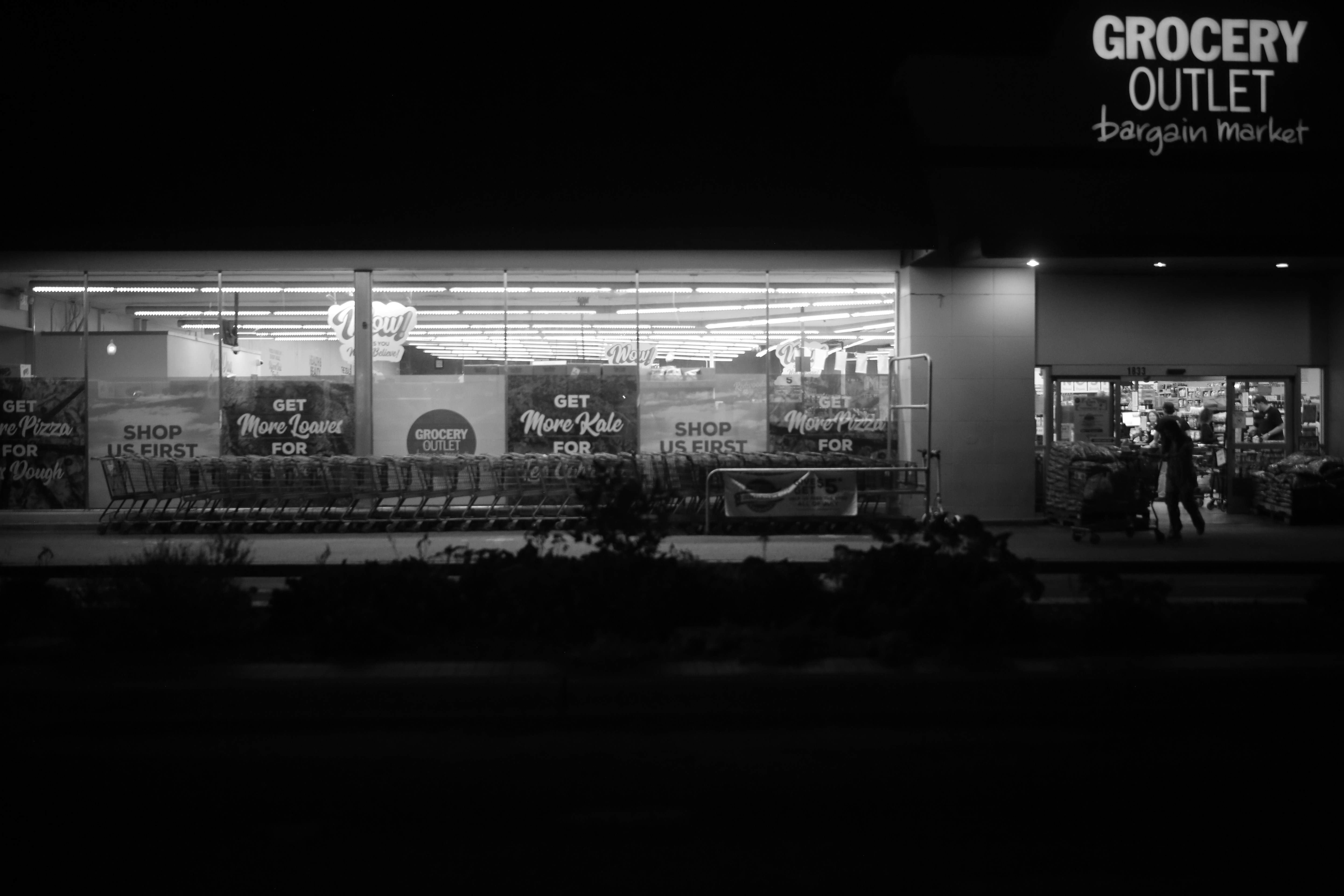 Neon Reflections Through Glass: Silent Shoppers at a Grocery Outlet After Dark