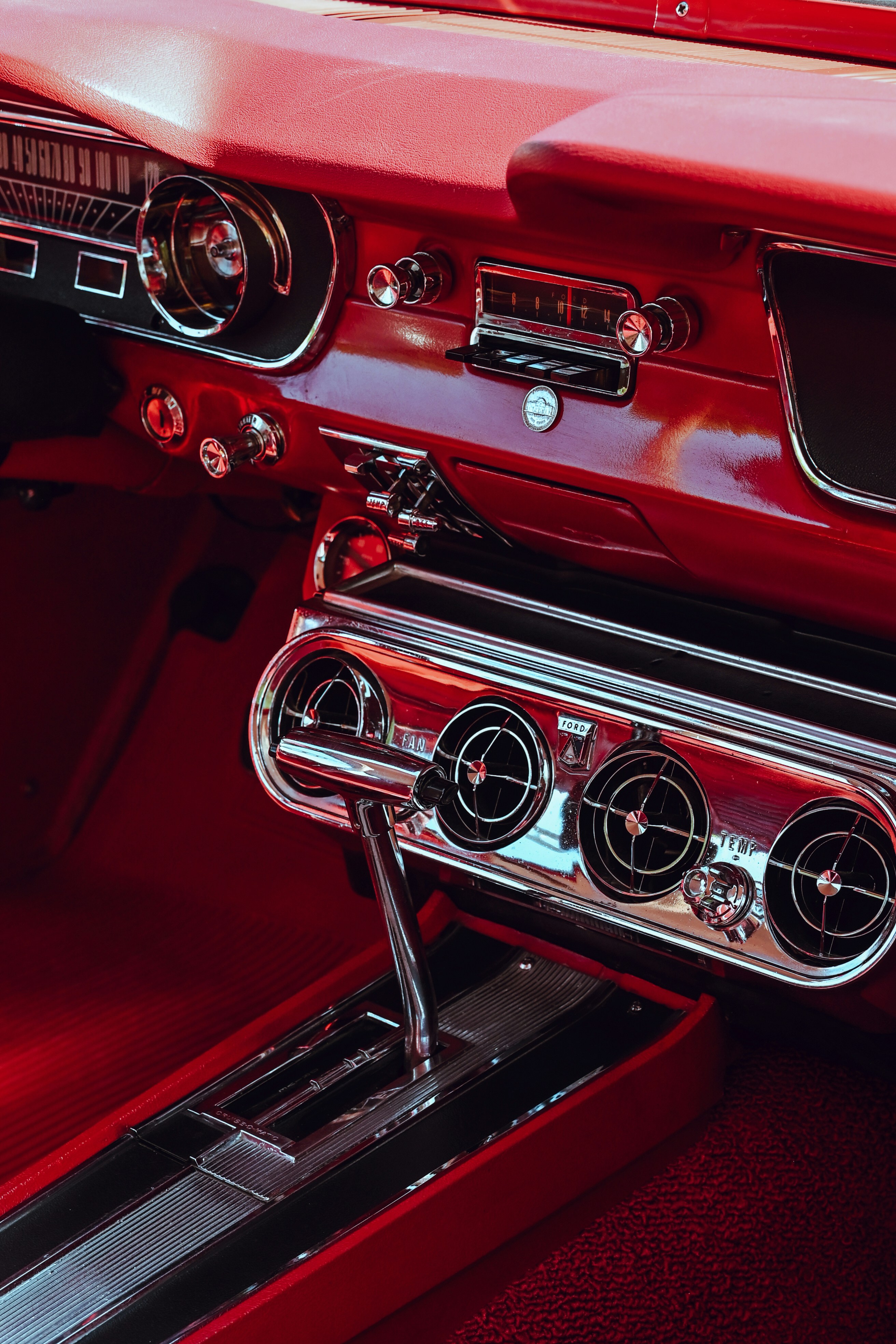 Interior view of a classic car showcasing a vibrant red dashboard and chrome accents, highlighting the intricate details of vintage automotive craftsmanship.