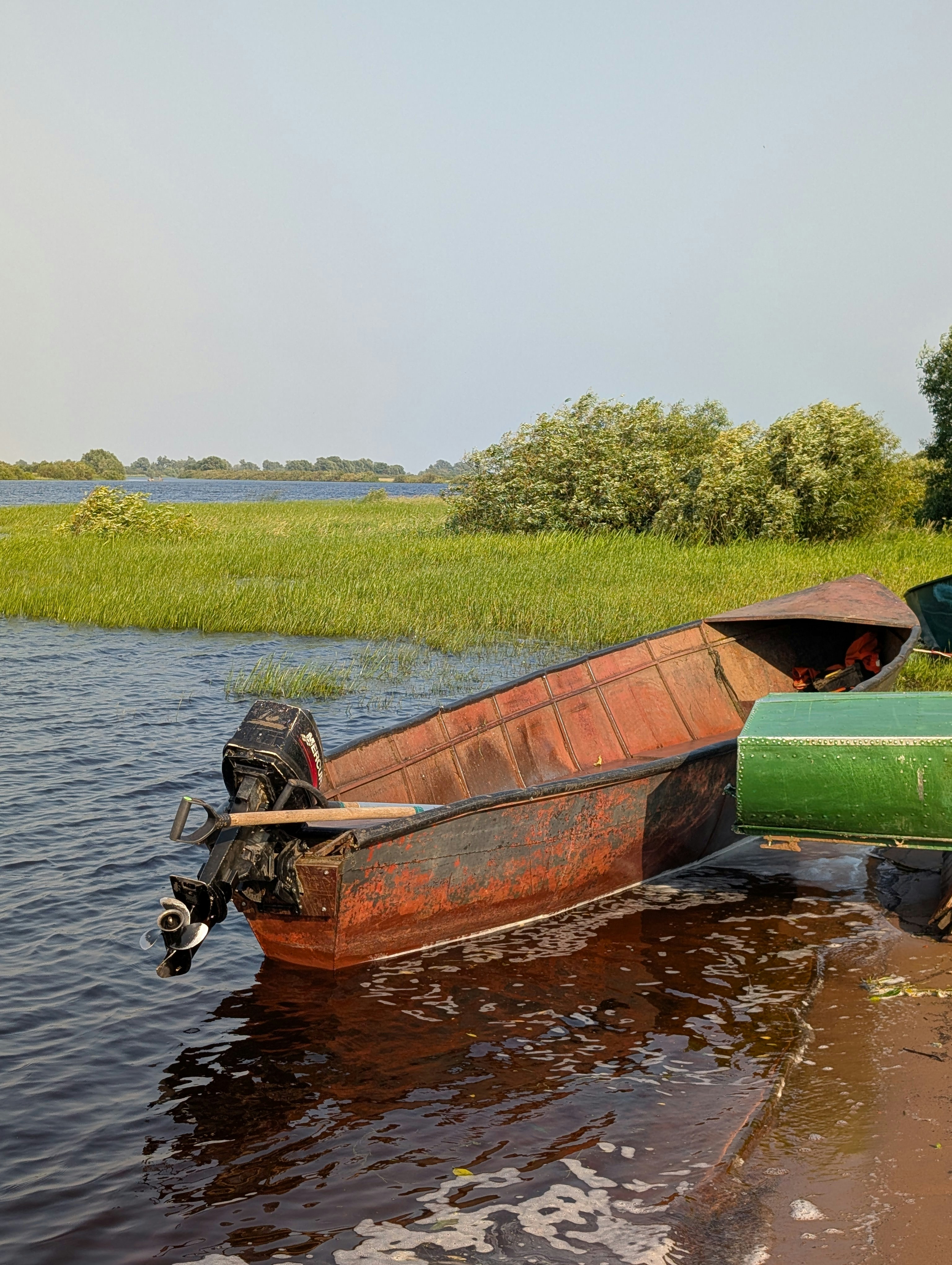 A fishing boat on the shore of the Ilmen lake in Vzvad village, Novgorod region | A rustic boat rests on the water's edge.