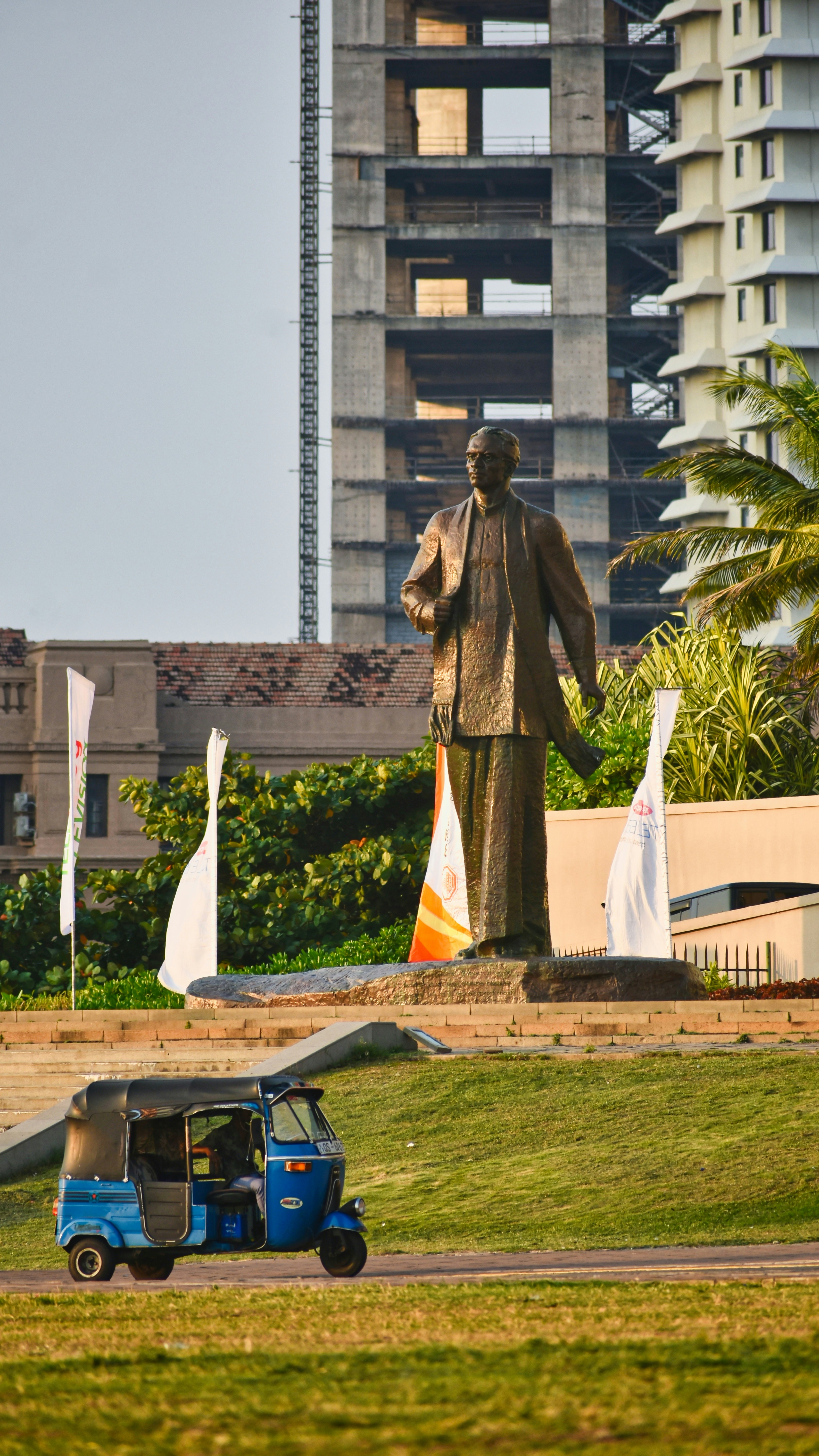 A statue, tuk-tuk, and buildings in the city.