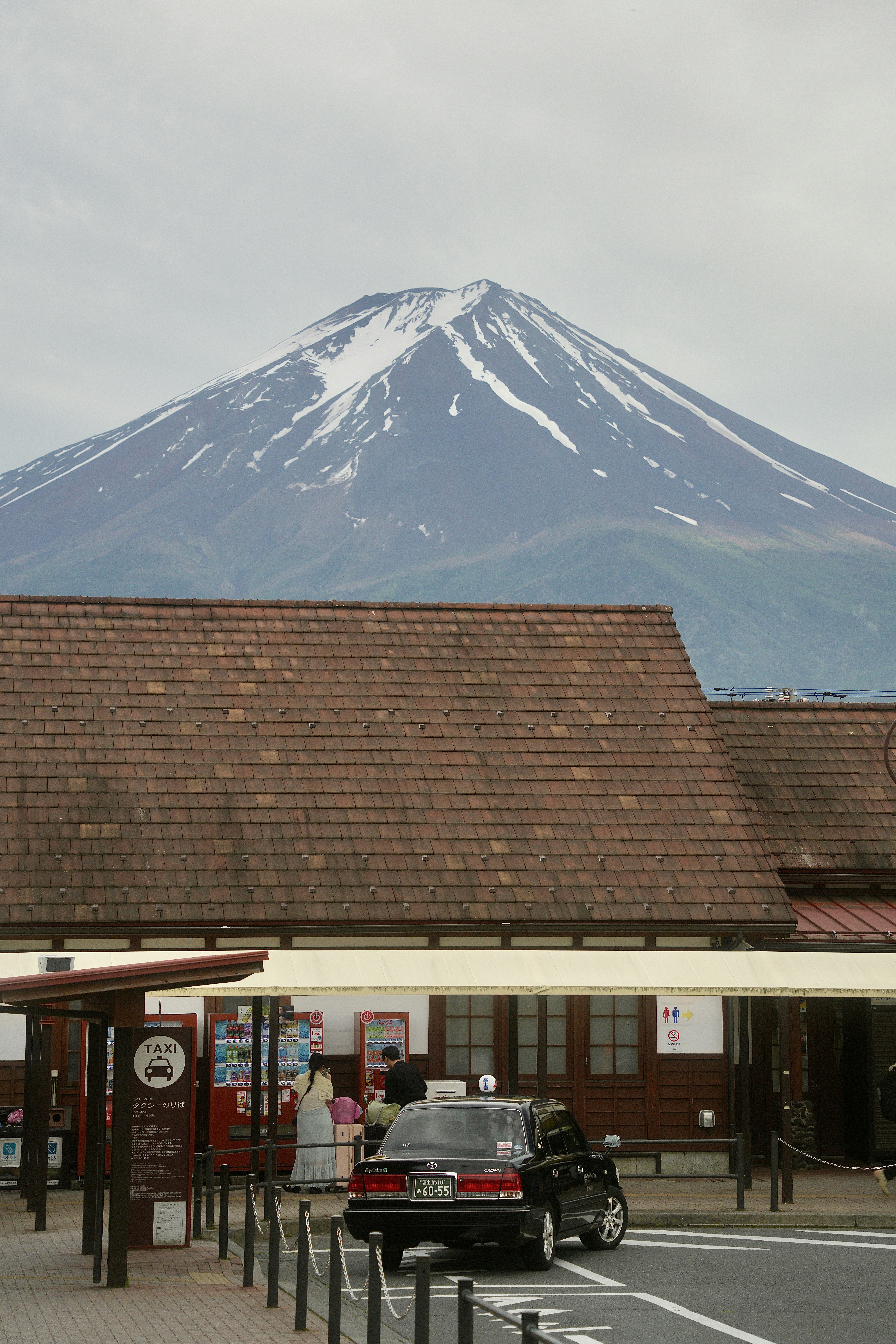 Kawaguchiko Station | Mount fuji towers over a building and taxi.