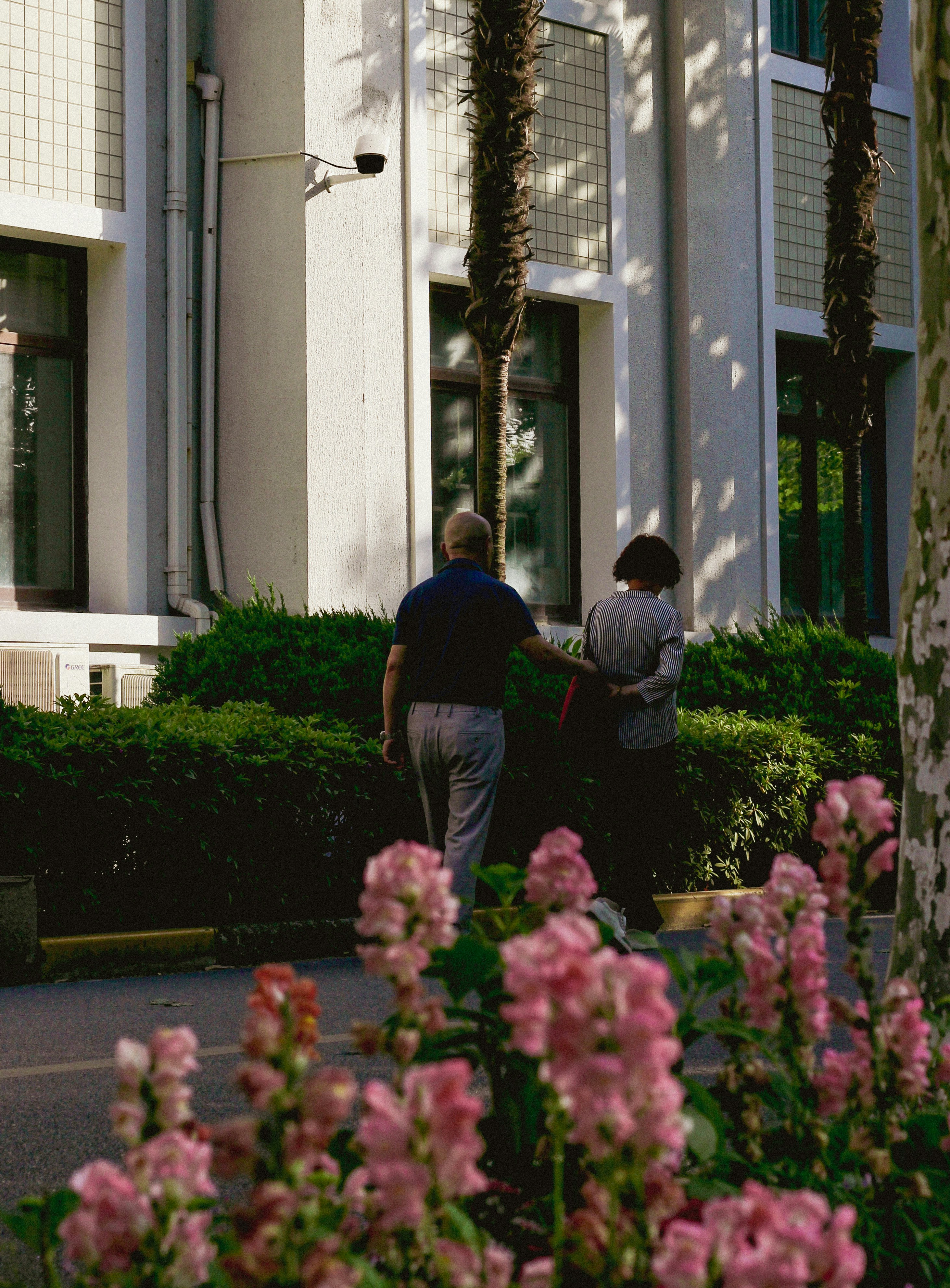 A couple walks along a building with flowers.