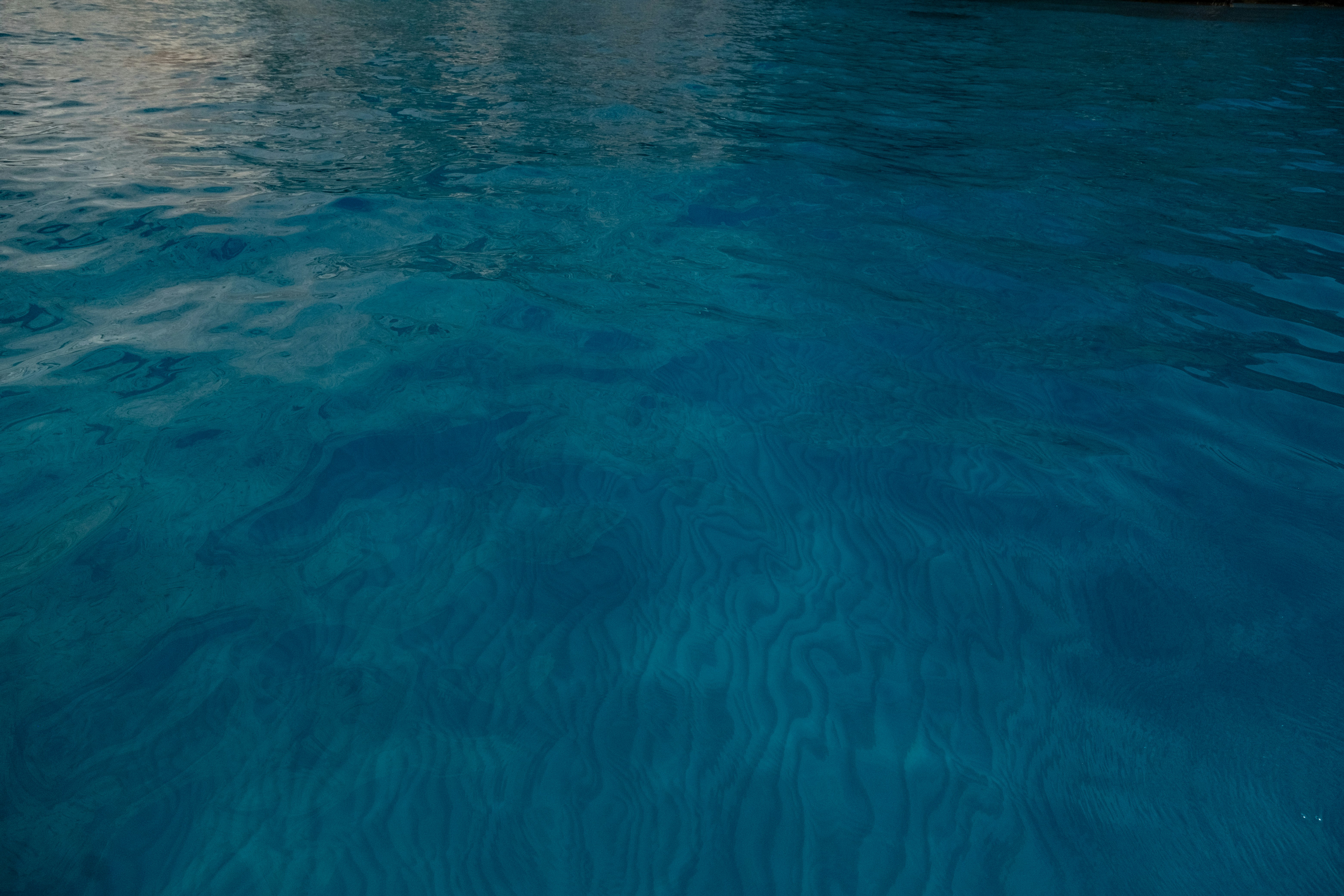 Crystal clear water surface reflecting subtle patterns and hues, evoking a sense of tranquility.