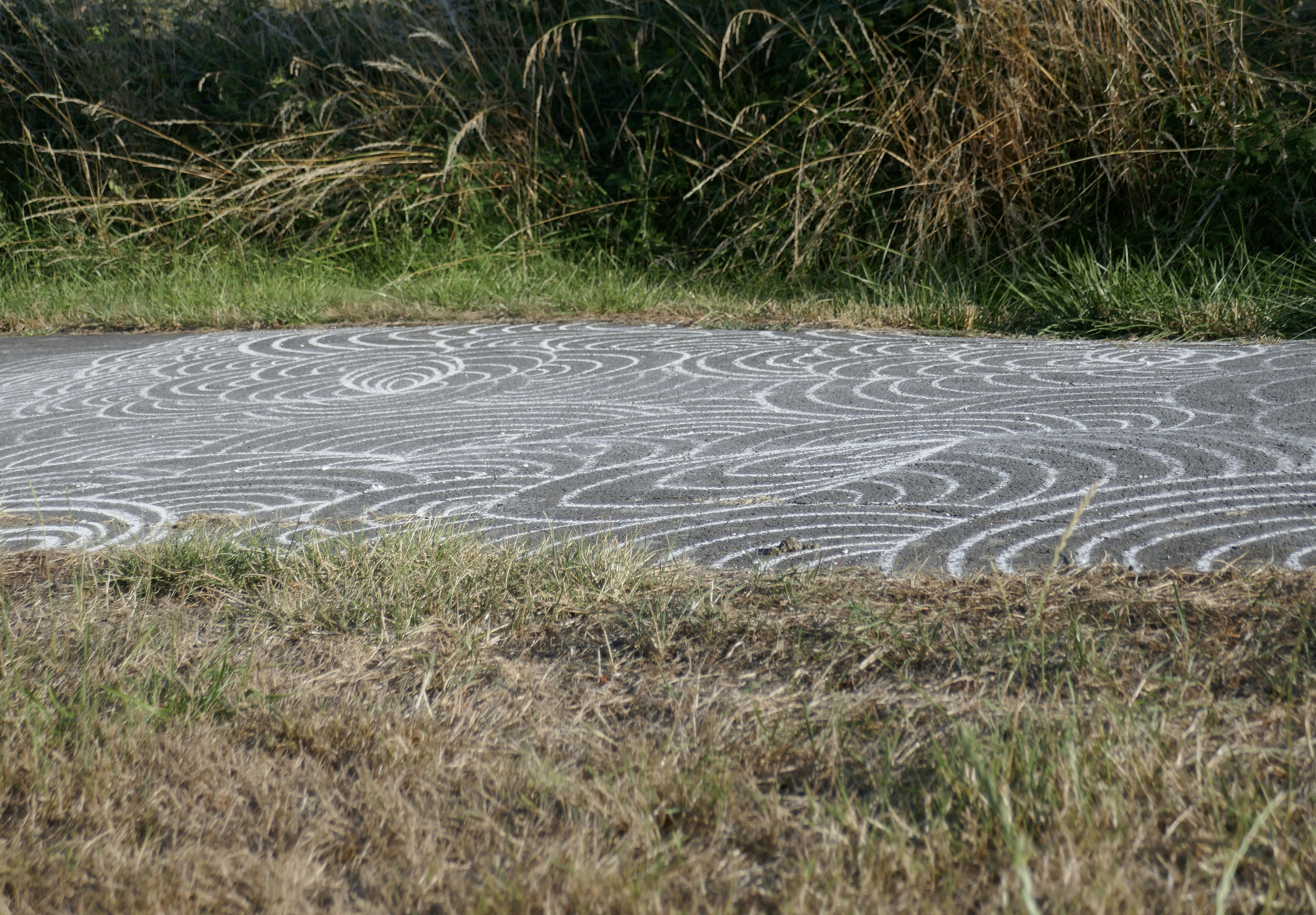 Trouée humaine dans verdure Guy Grandjean Hugo Rouges Jardins | A road with decorative, spiraling patterns.