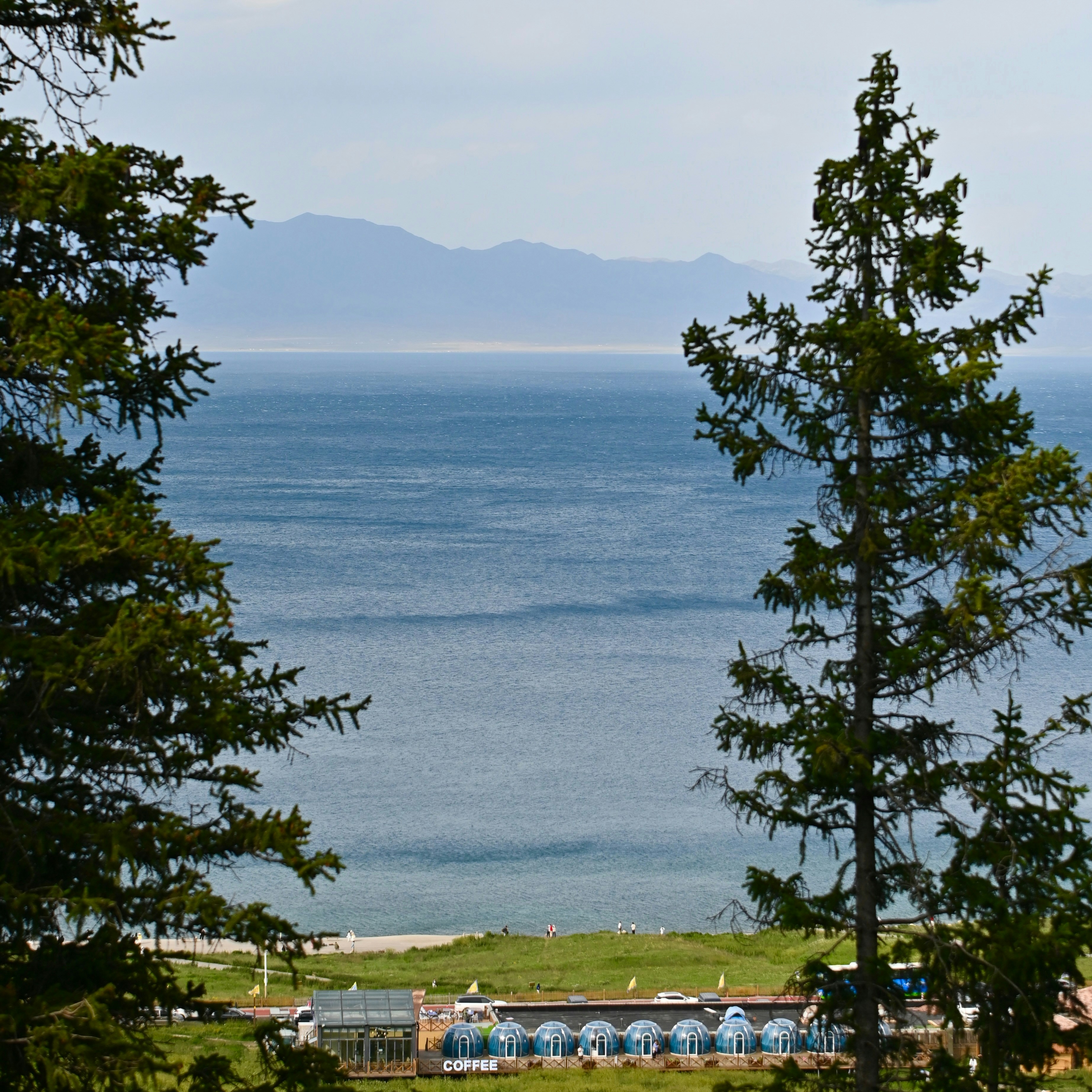 Lush greenery frames a tranquil beach scene where the ocean meets the horizon, dotted with distant mountains. The setting invites relaxation and exploration.