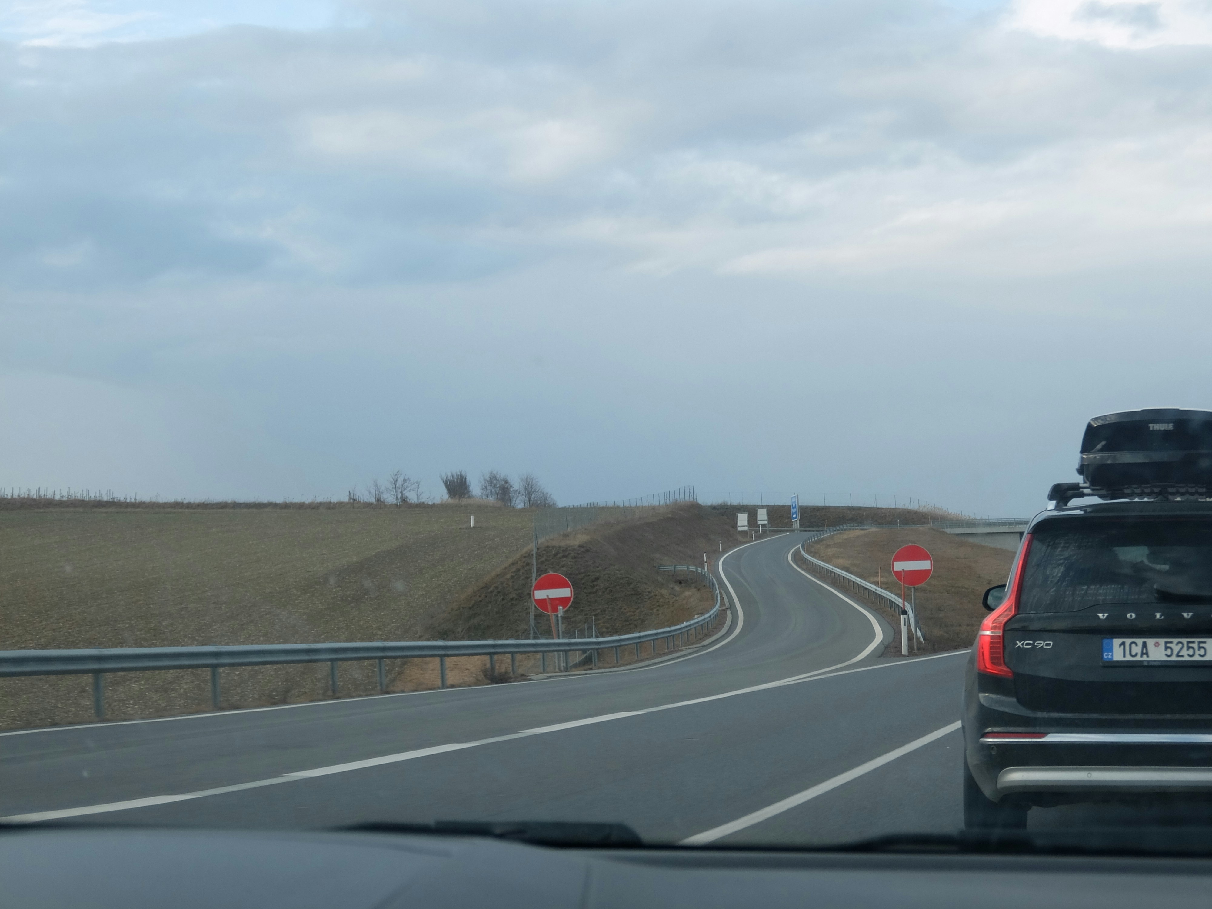 A car drives on a quiet highway under a cloudy sky.