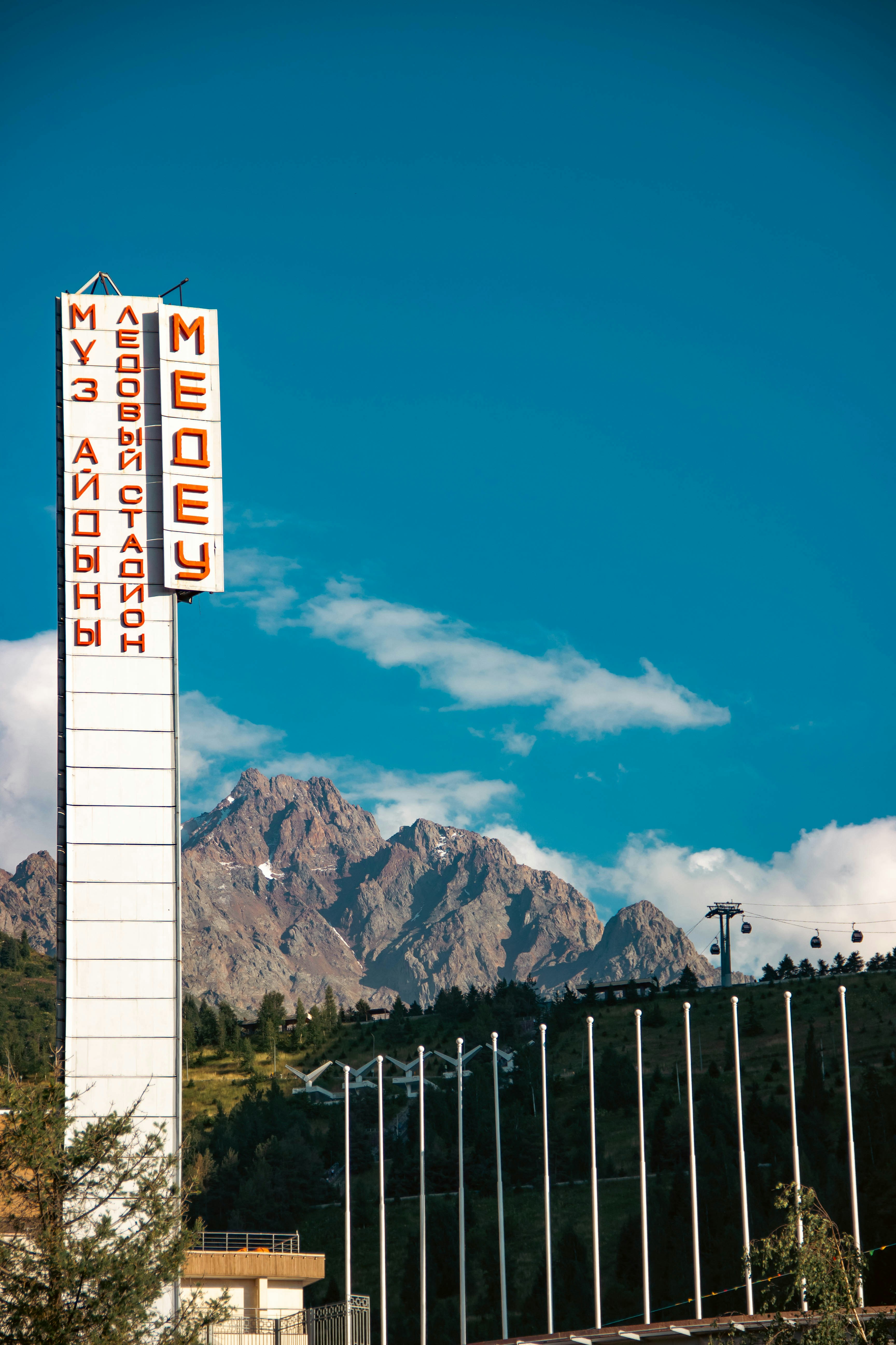 Vintage vertical marquee sign rising beside rugged Alpine peaks under a cobalt sky