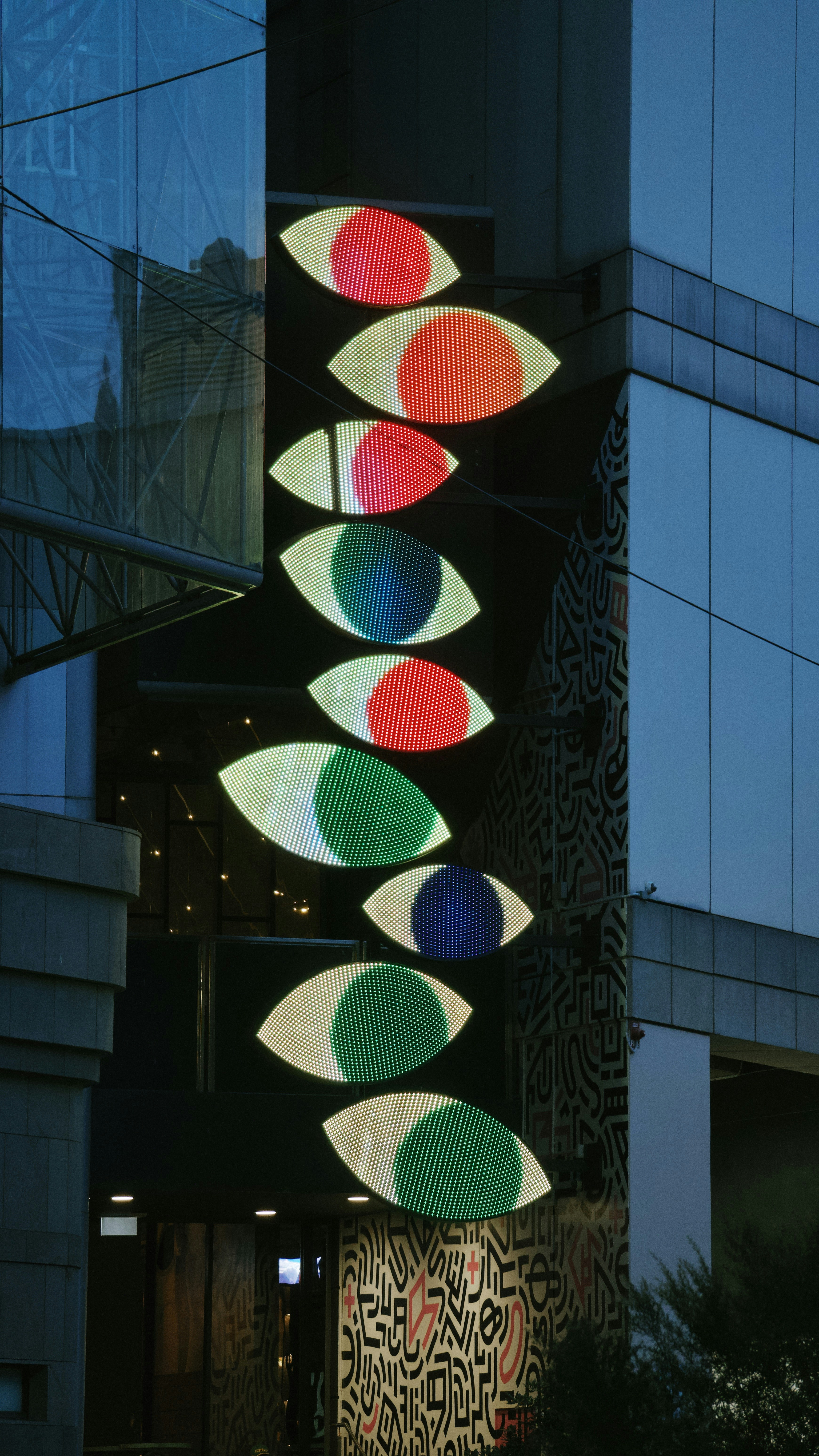 Vibrant LED display featuring a series of stylized eyes in alternating colors, set against a modern architectural backdrop.