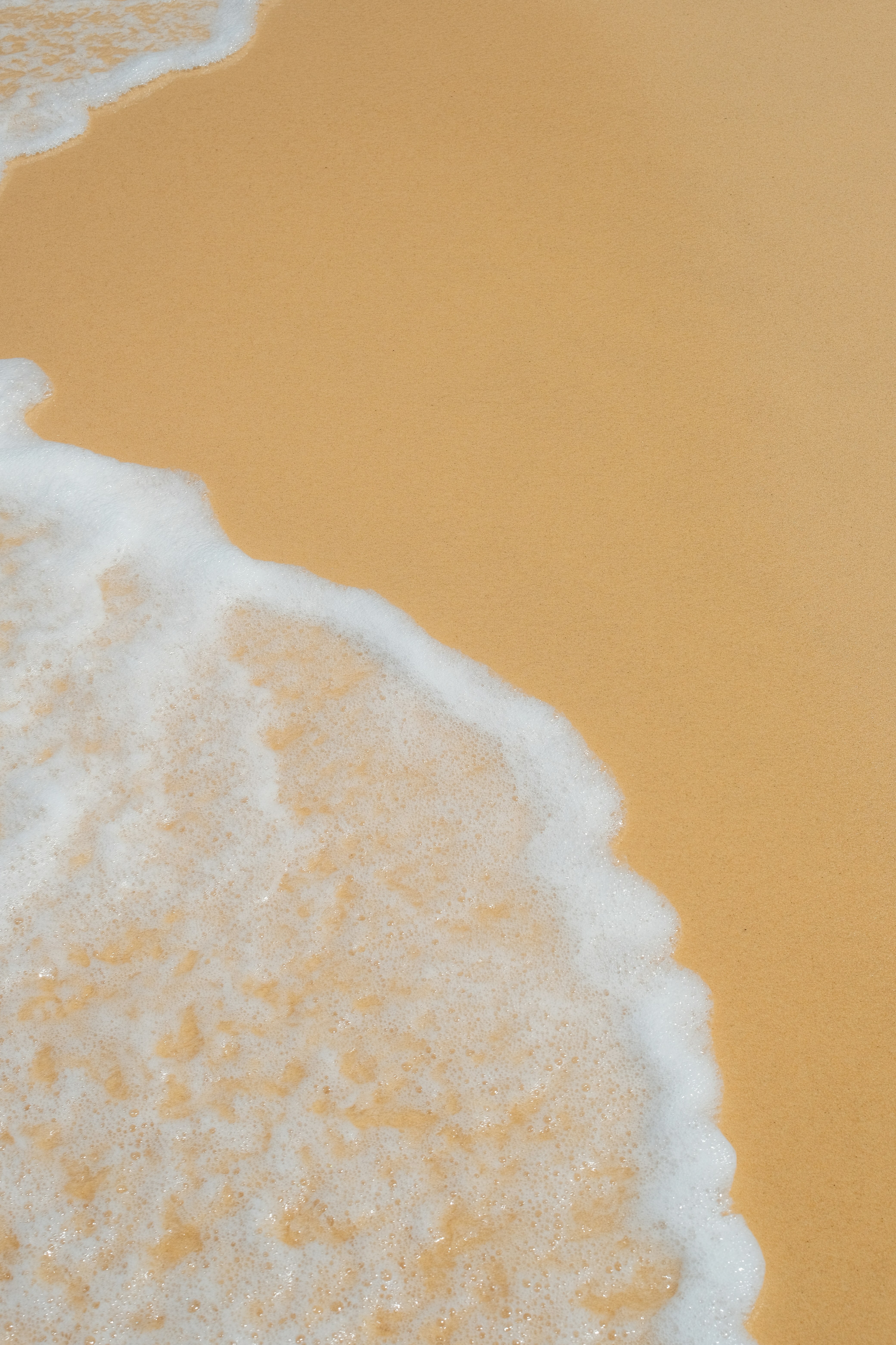 Gentle waves caressing a sandy beach, creating a serene coastal scene. The foam dances on the golden sand.