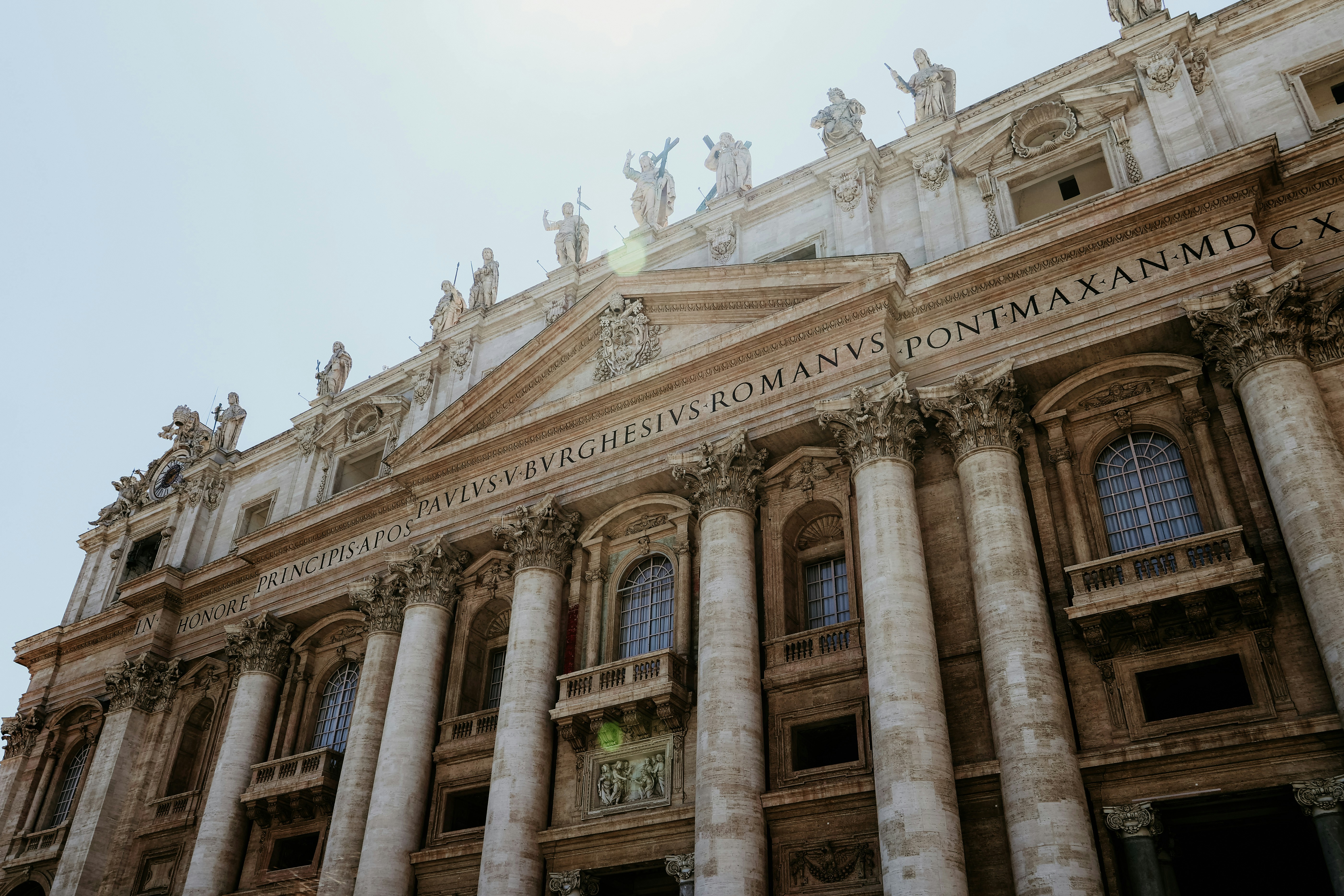 Intricate architectural details of a grand building, showcasing classical columns and sculptures under a bright sky.