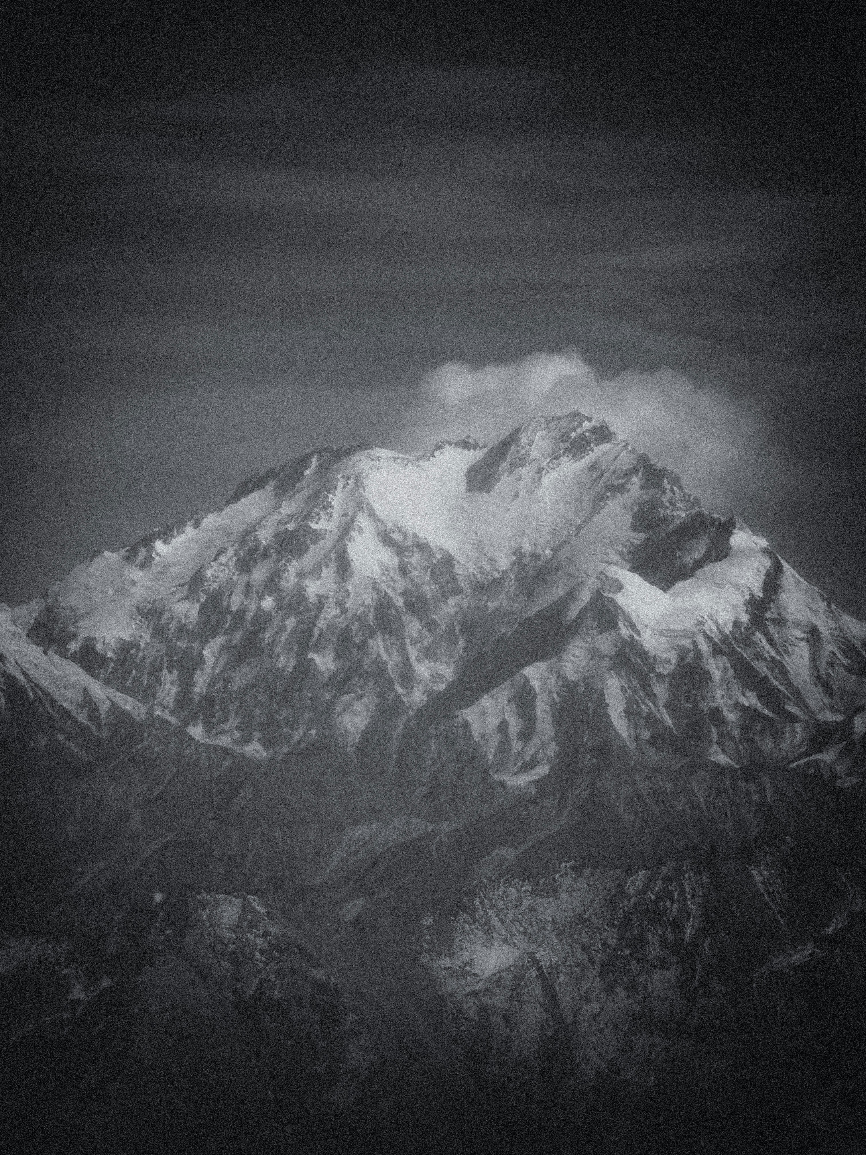 Monochromatic view of a towering snow-capped mountain against a moody sky, showcasing the rugged beauty of nature's peaks.