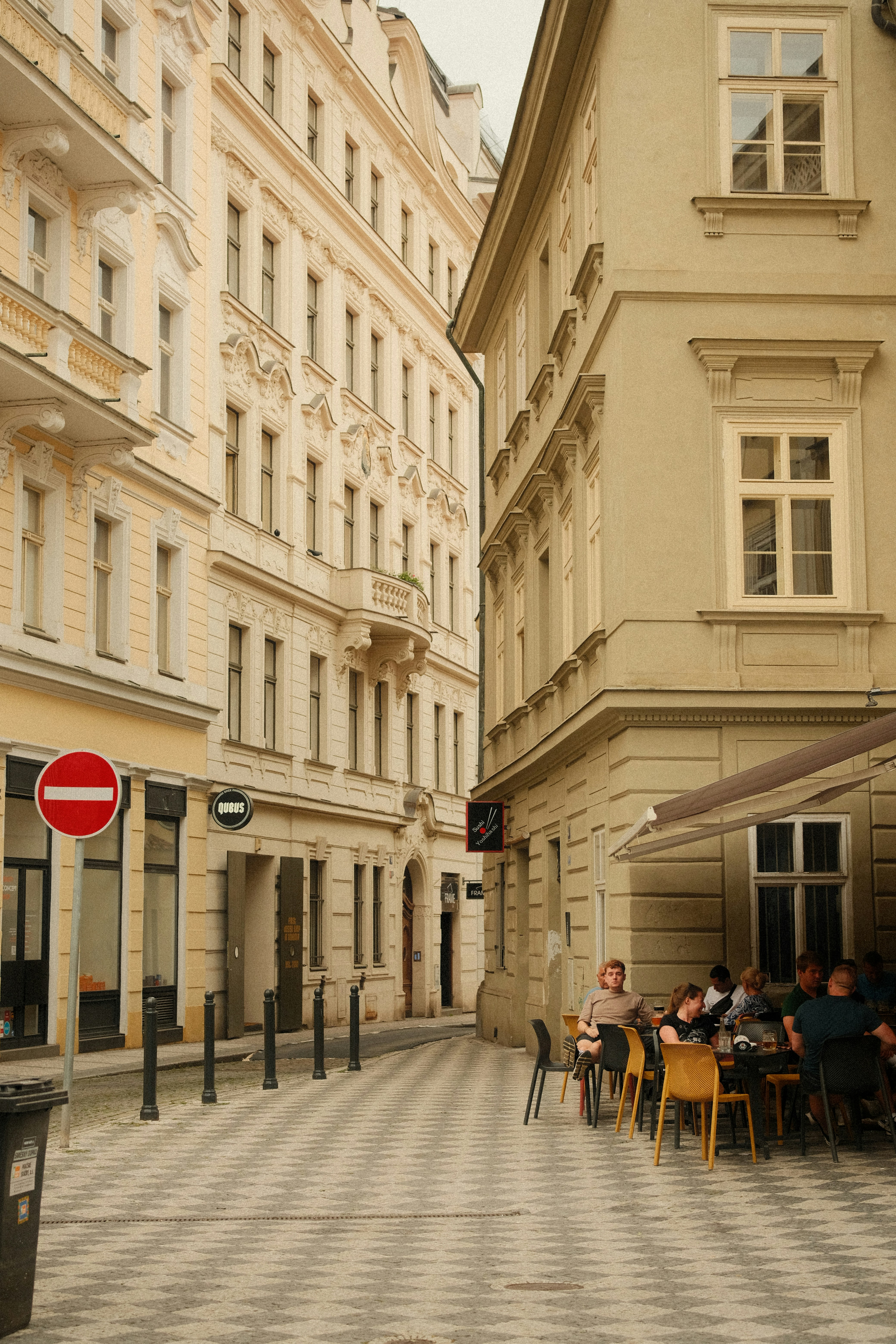 Narrow street with outdoor dining in an urban setting | Buildings and a cafe line a cobbled street.