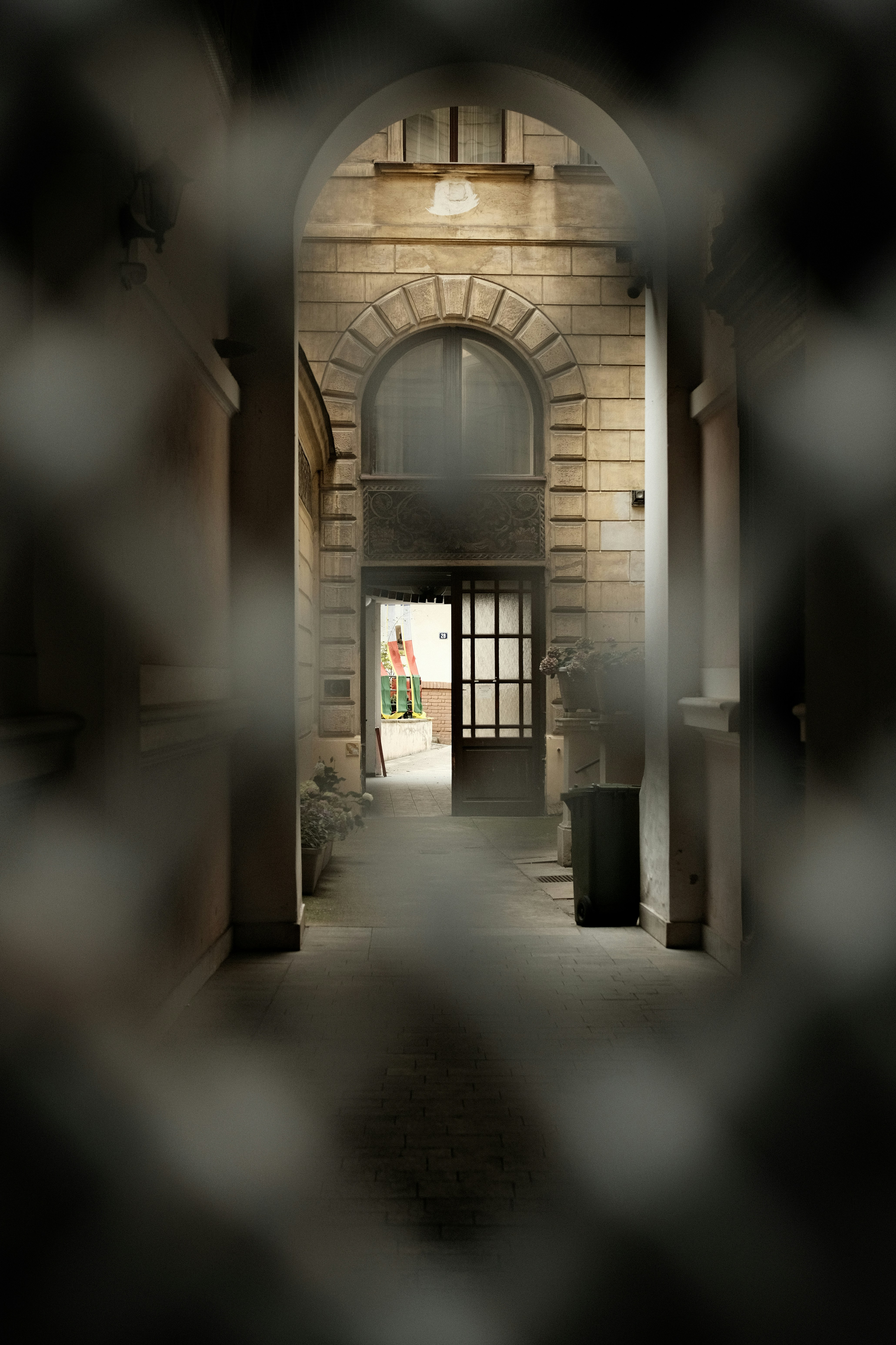 View of an alley through mesh fencing in a city | An open doorway reveals a light-filled courtyard.
