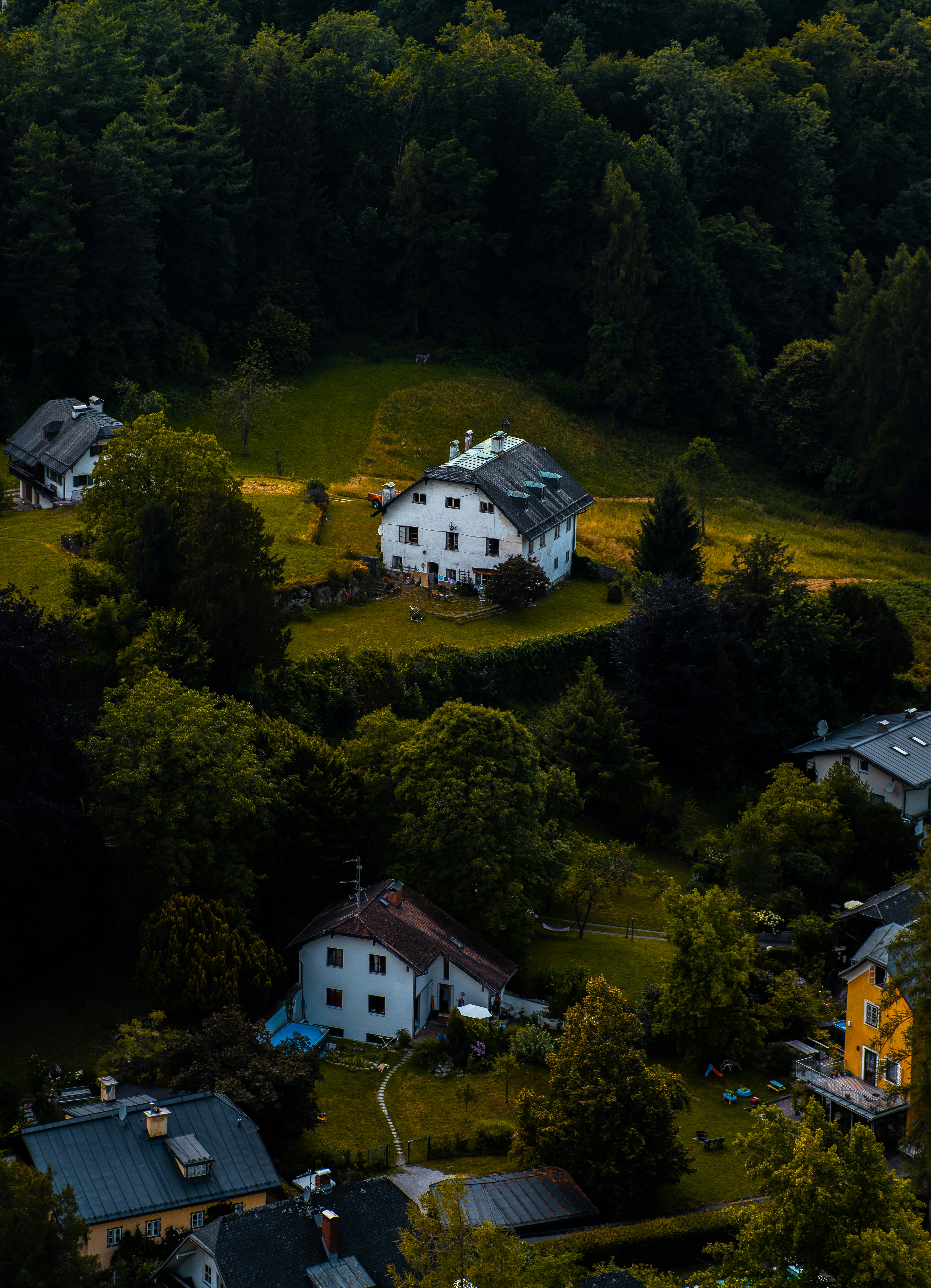 A serene landscape showcasing a cluster of houses nestled among lush greenery, with a prominent white building standing out against the backdrop of dense trees.