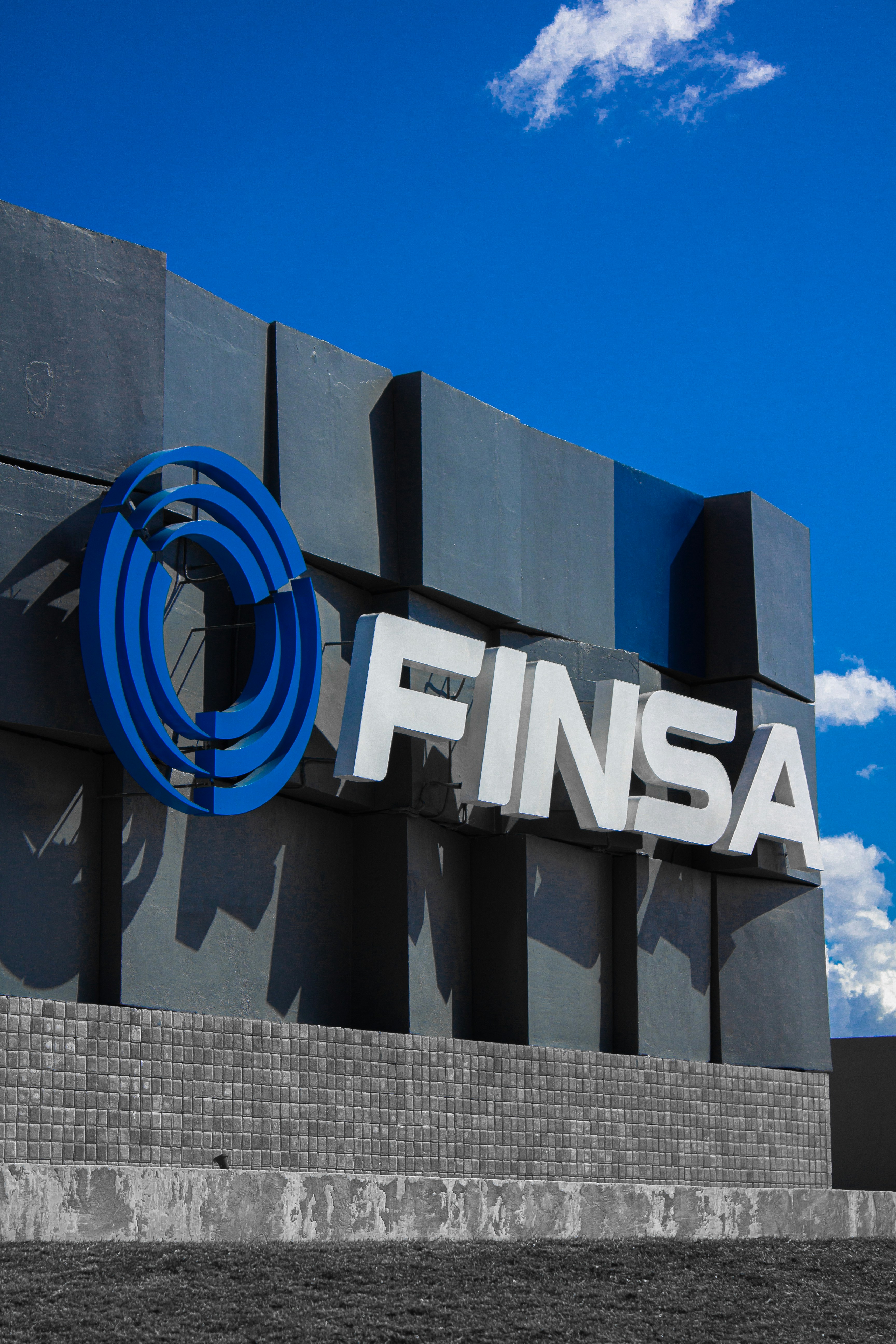 Prominent blue and white Finsa logo displayed on a modern gray wall against a bright blue sky.
