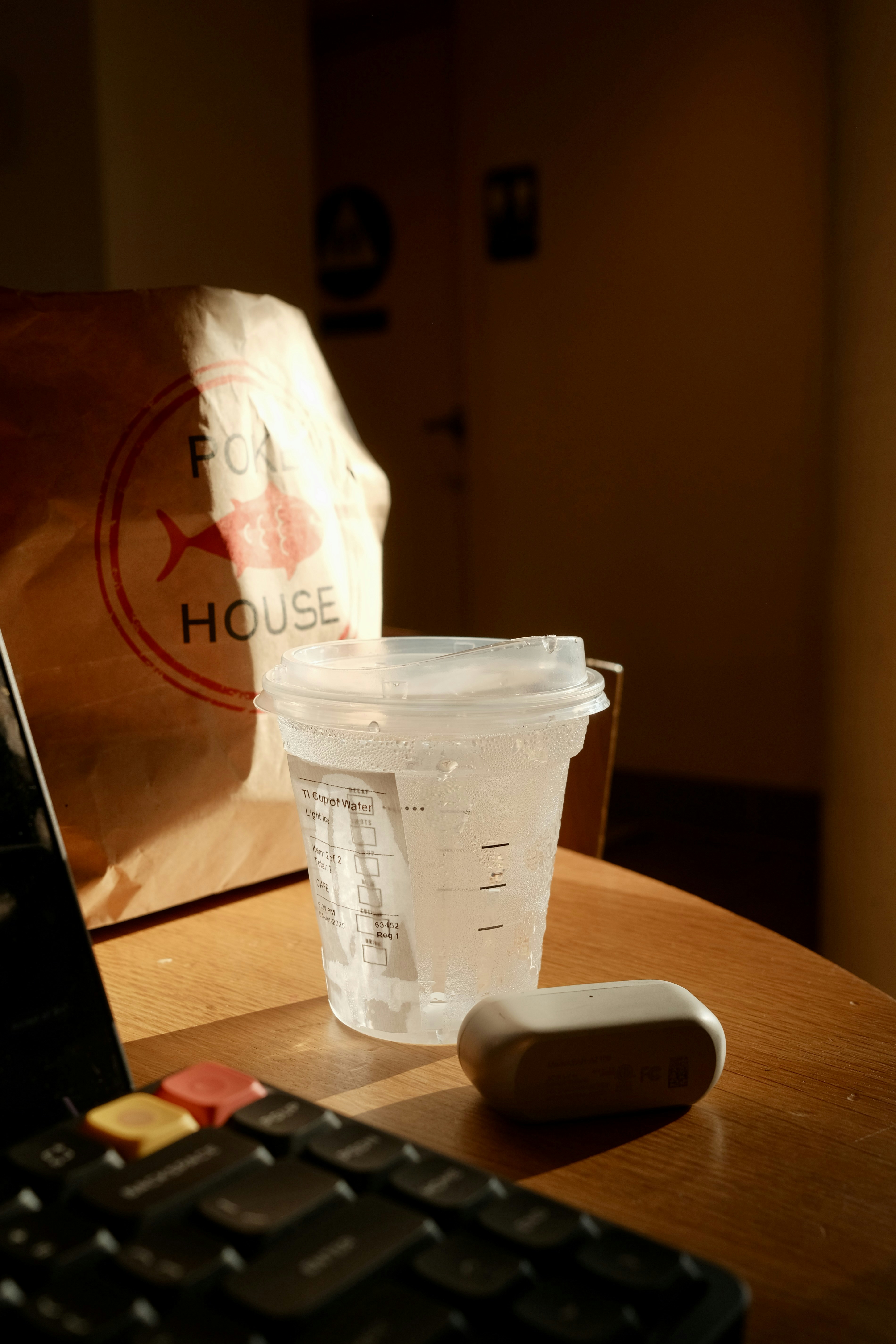 Tungsten Glow Still Life: Translucent Cup, Paper Bag, and Keyboard on a Quiet Desk