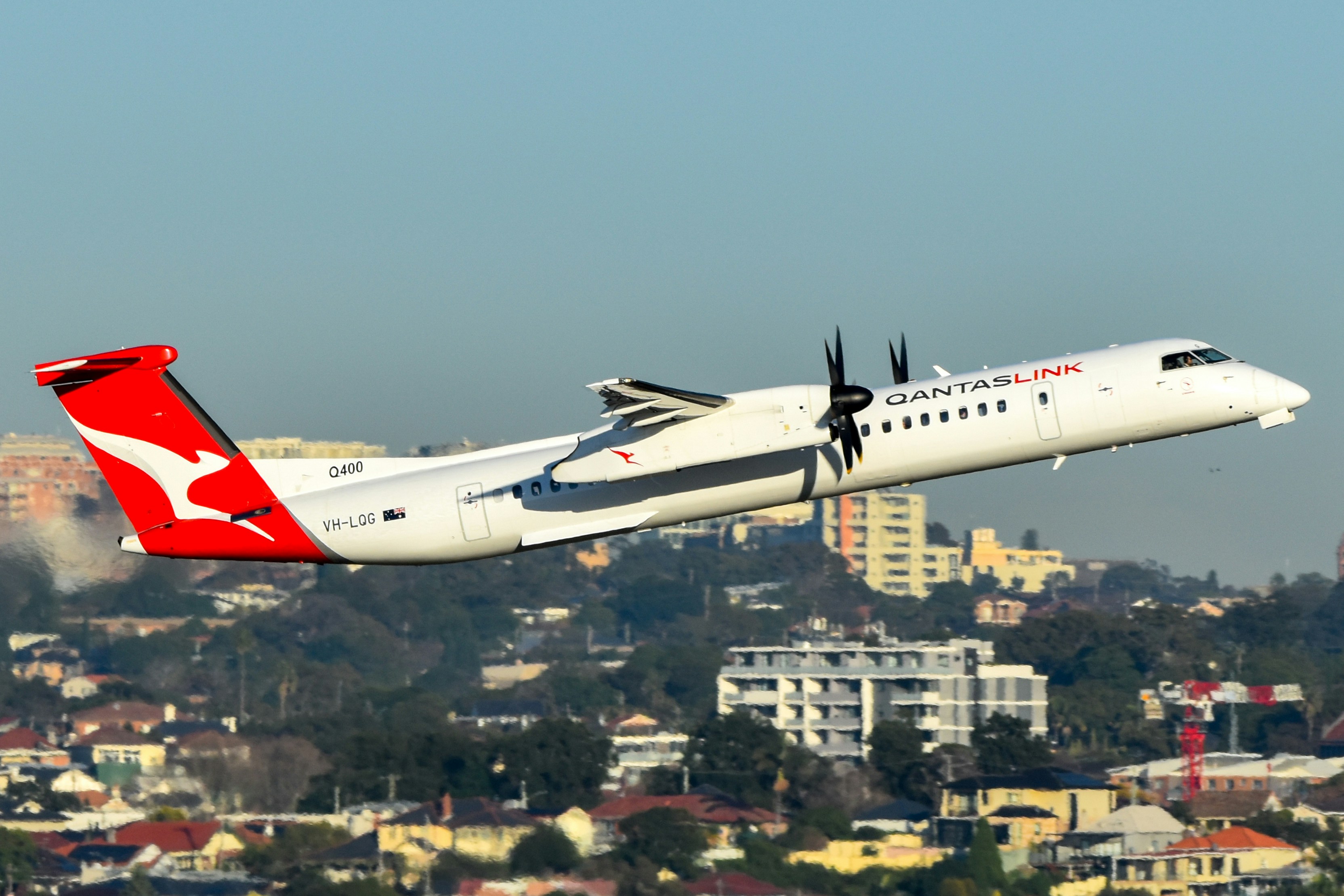 A QantasLink Q400 departing Sydney | A qantas plane takes off over a cityscape.