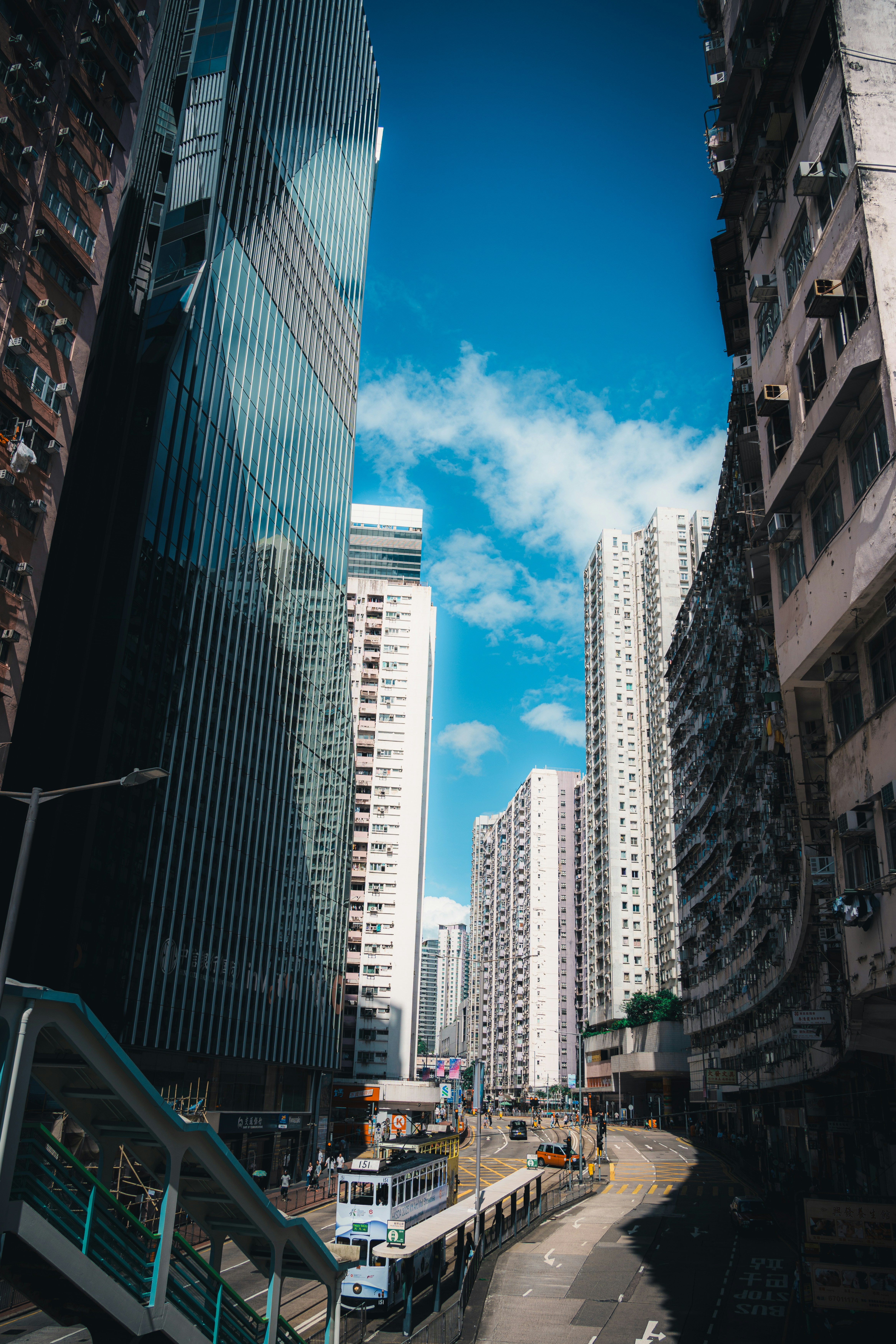A vibrant cityscape showcasing towering skyscrapers, with a tram navigating the bustling street below. The bright blue sky contrasts with the architectural lines.