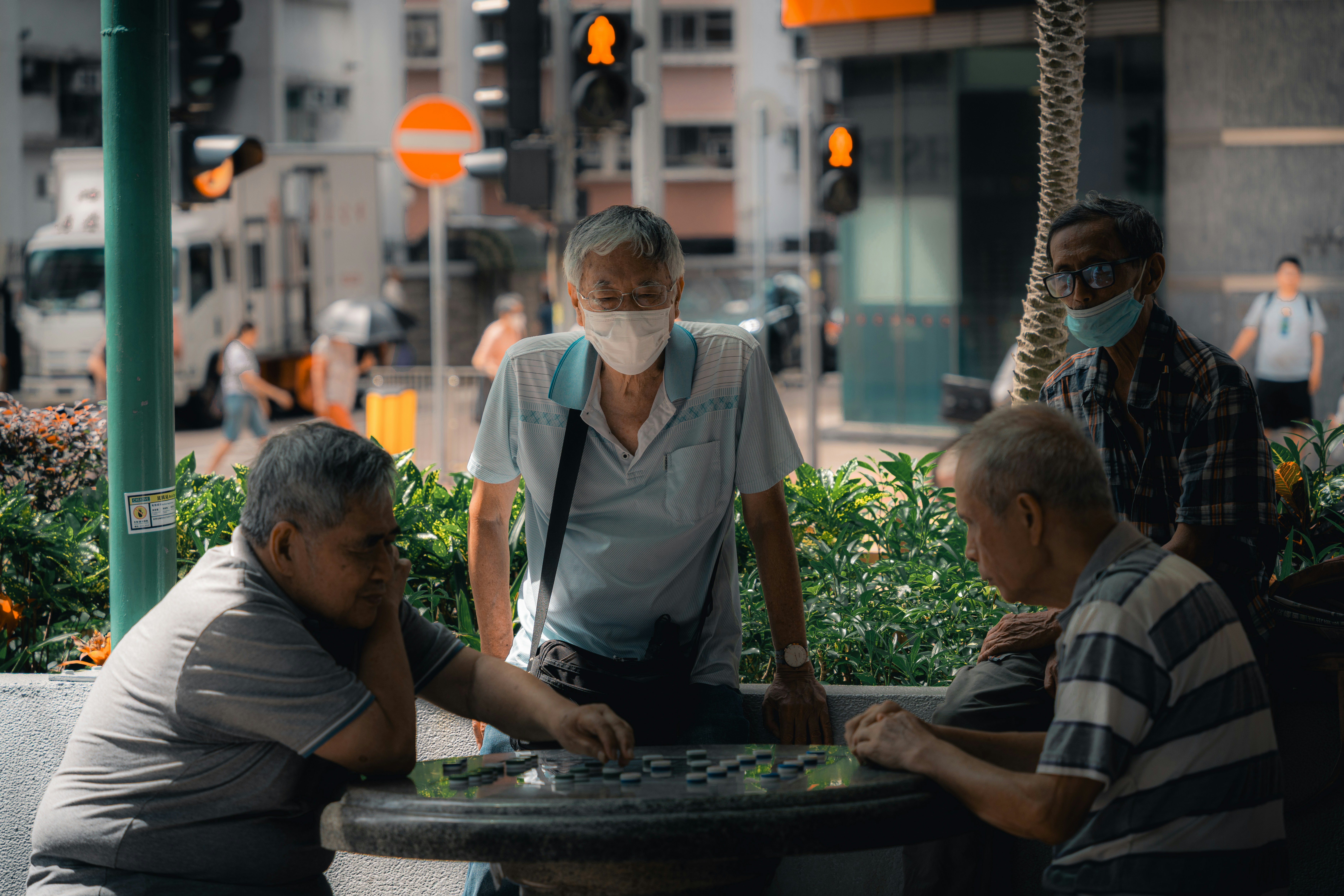 Elderly men engaged in a game of checkers at a bustling urban park, surrounded by vibrant greenery and city life.