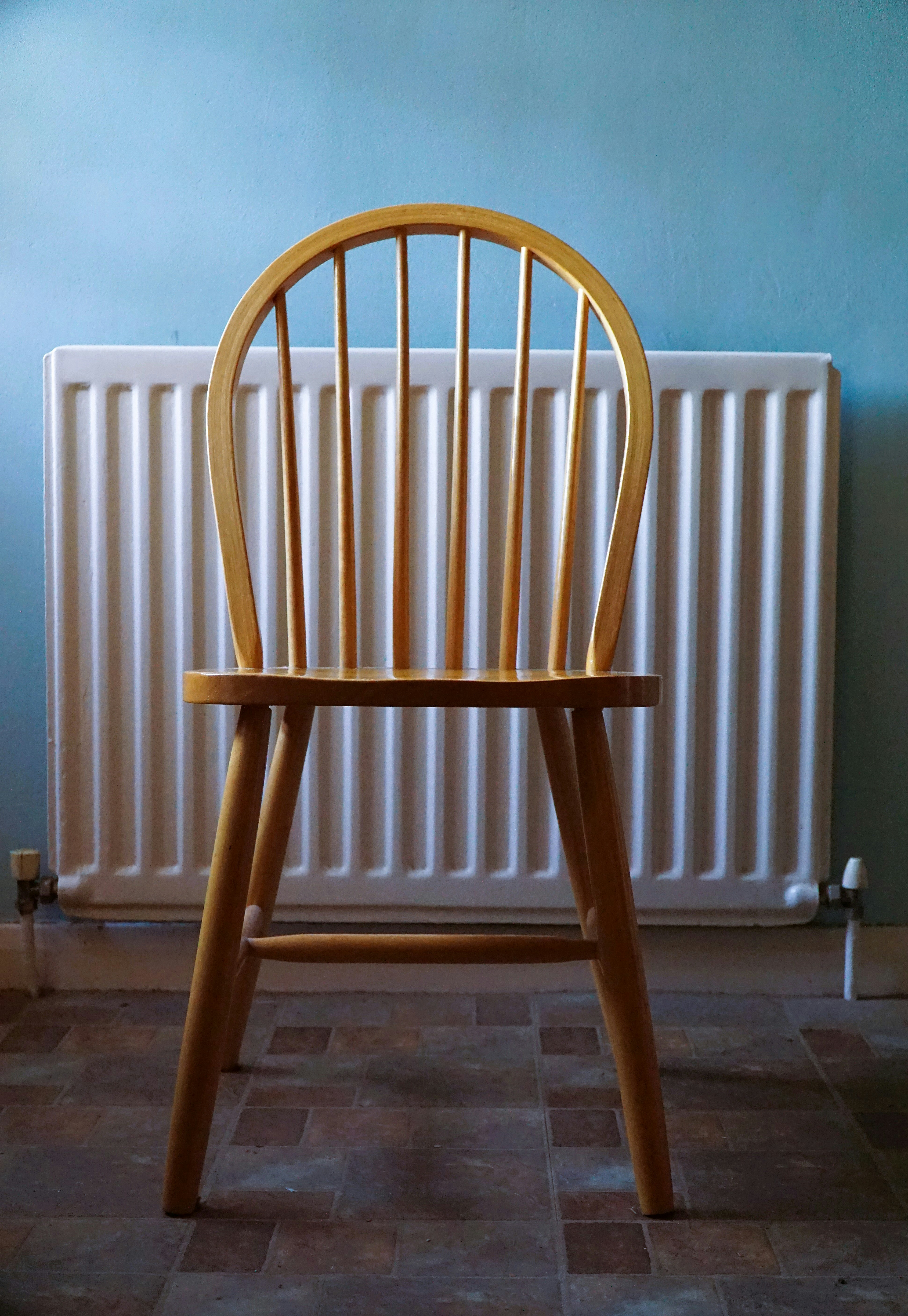 A wooden chair positioned in front of a radiator against a soft blue wall, highlighting its simple design and functionality.