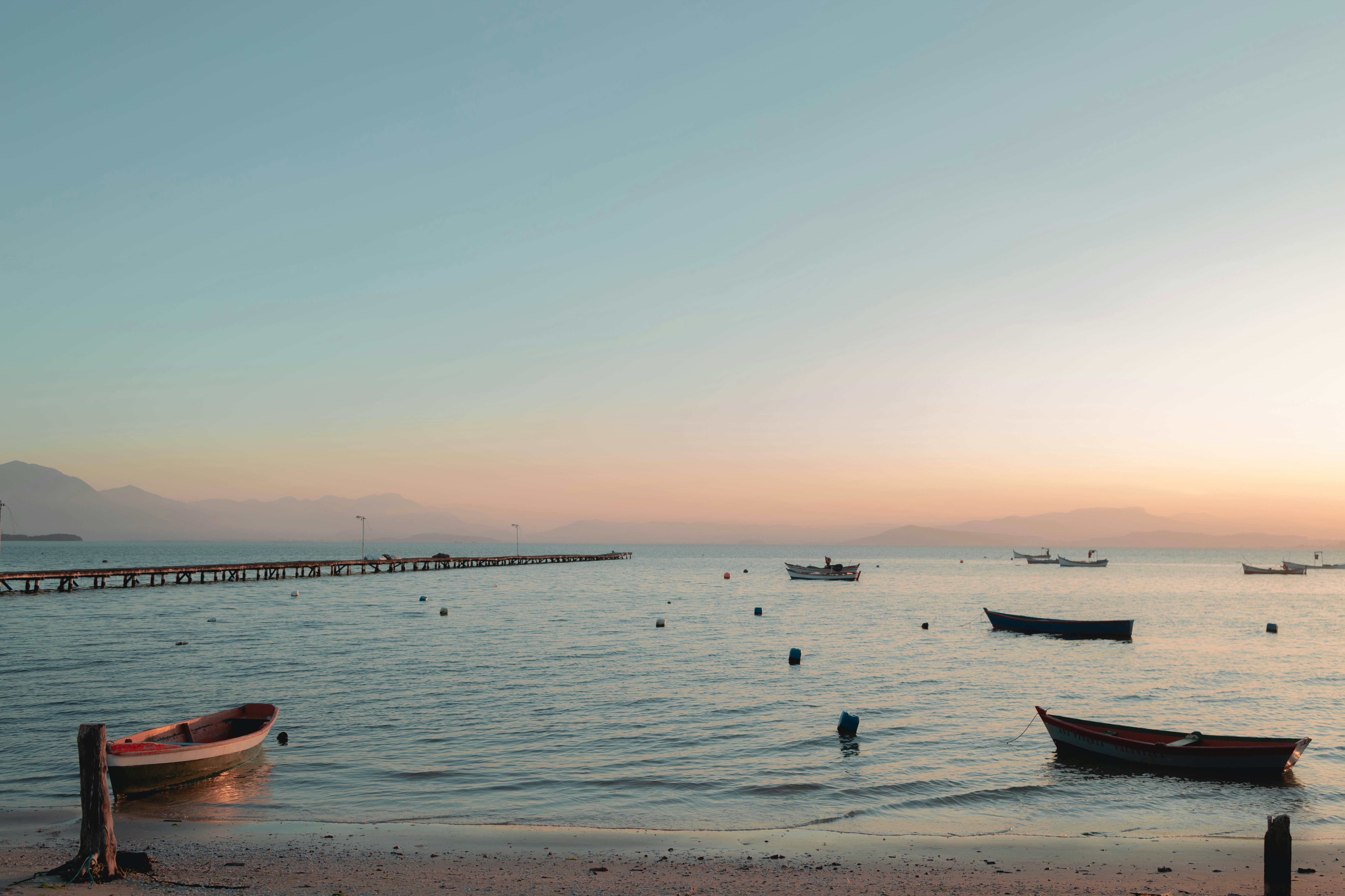 Pier at Dusk: Boats Drift Under a Peach-Sky Horizon