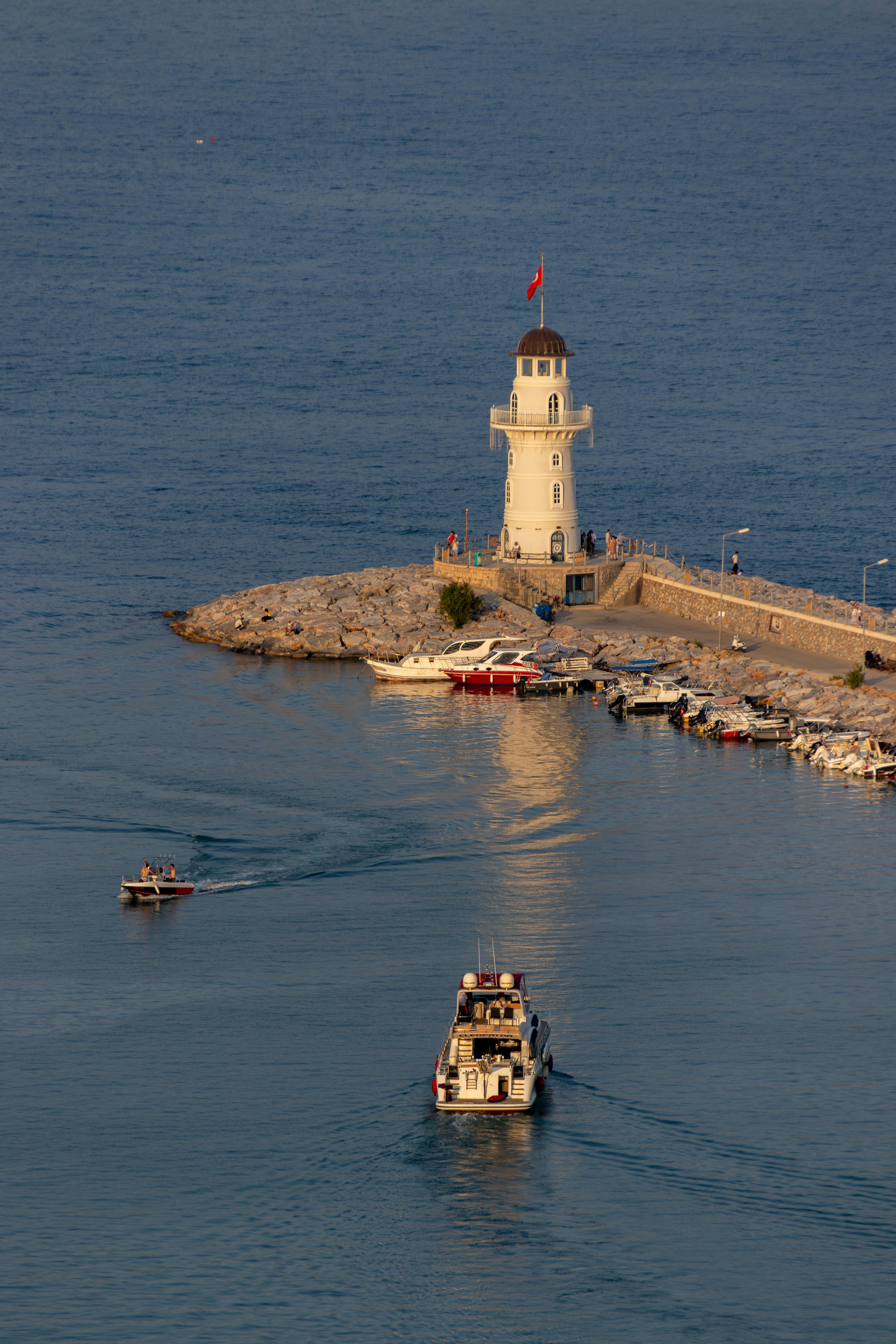 A lighthouse standing proudly on a rocky outcrop, surrounded by calm waters and boats navigating the harbor.