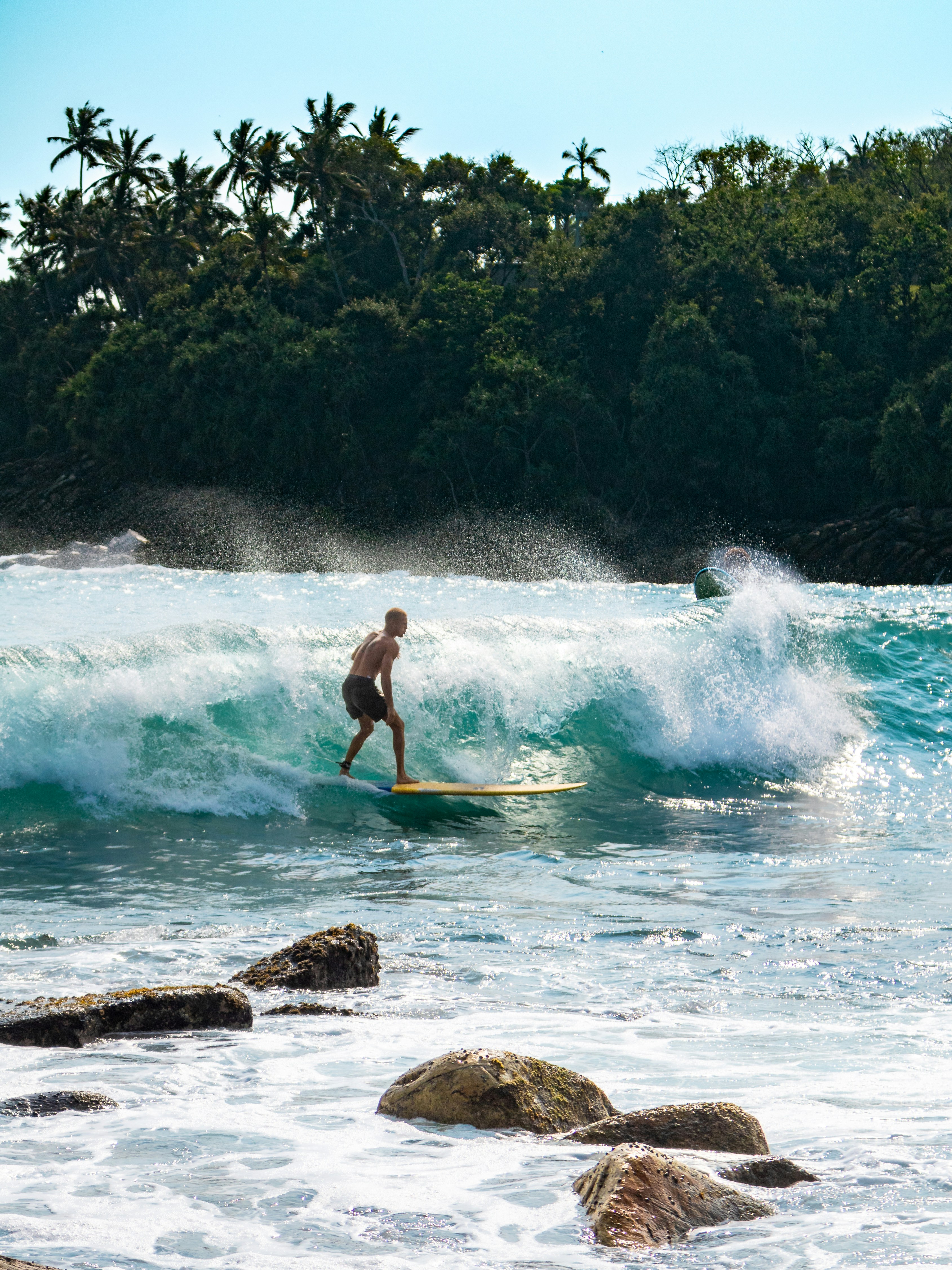 The horseshoe-shaped bay known as Hiriketiya Beach is one of the best surfing spots on the south coast of Sri Lanka. It’s unique in that despite it’s small size, it has waves suitable for every level. Pictured here are people enjoying the surfing culture of the beach. | Surfer rides a wave near a tropical shoreline.